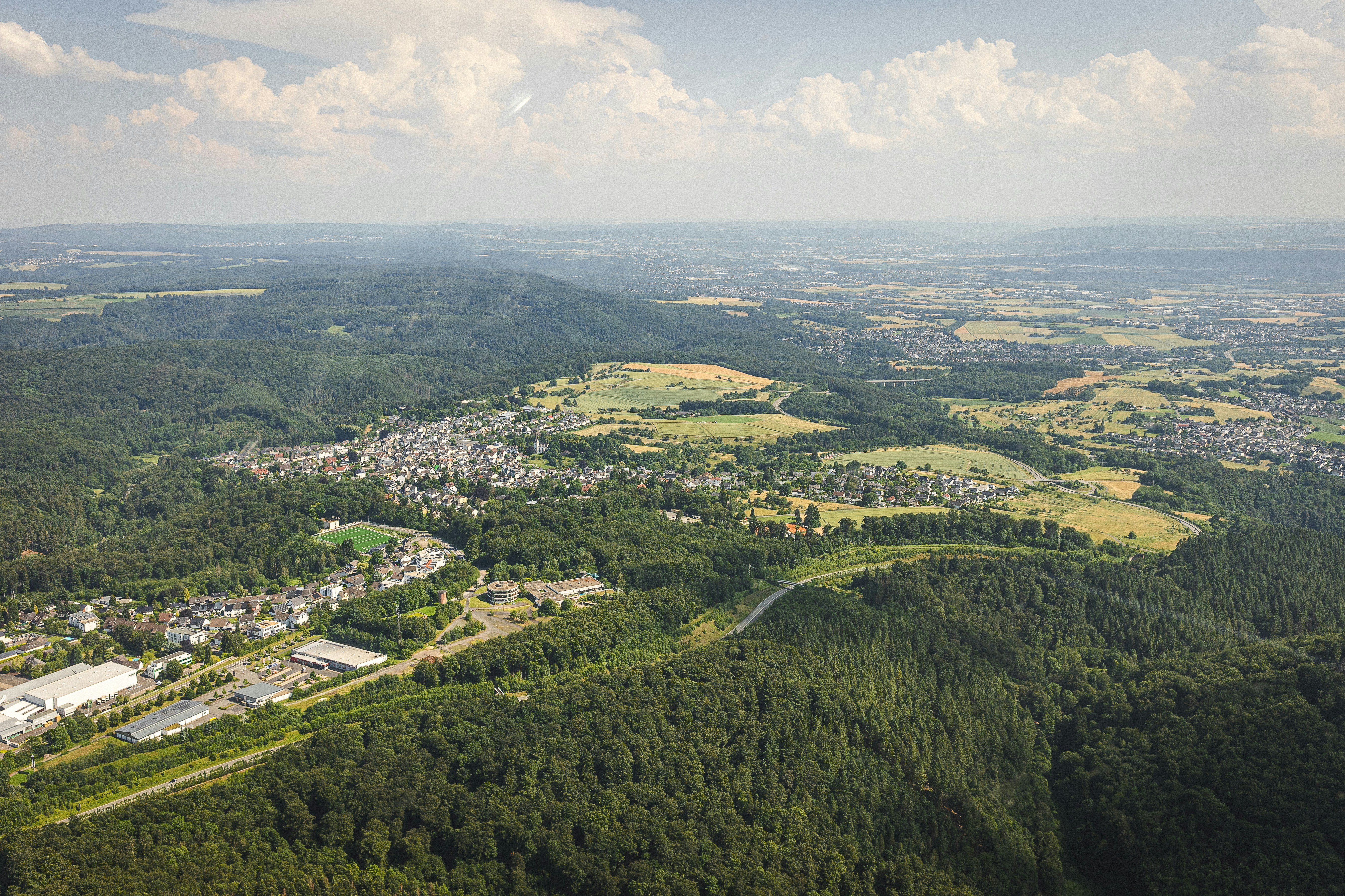 Aerial tapestry: a town nestled in rolling greens beneath a vast cloud-streaked sky