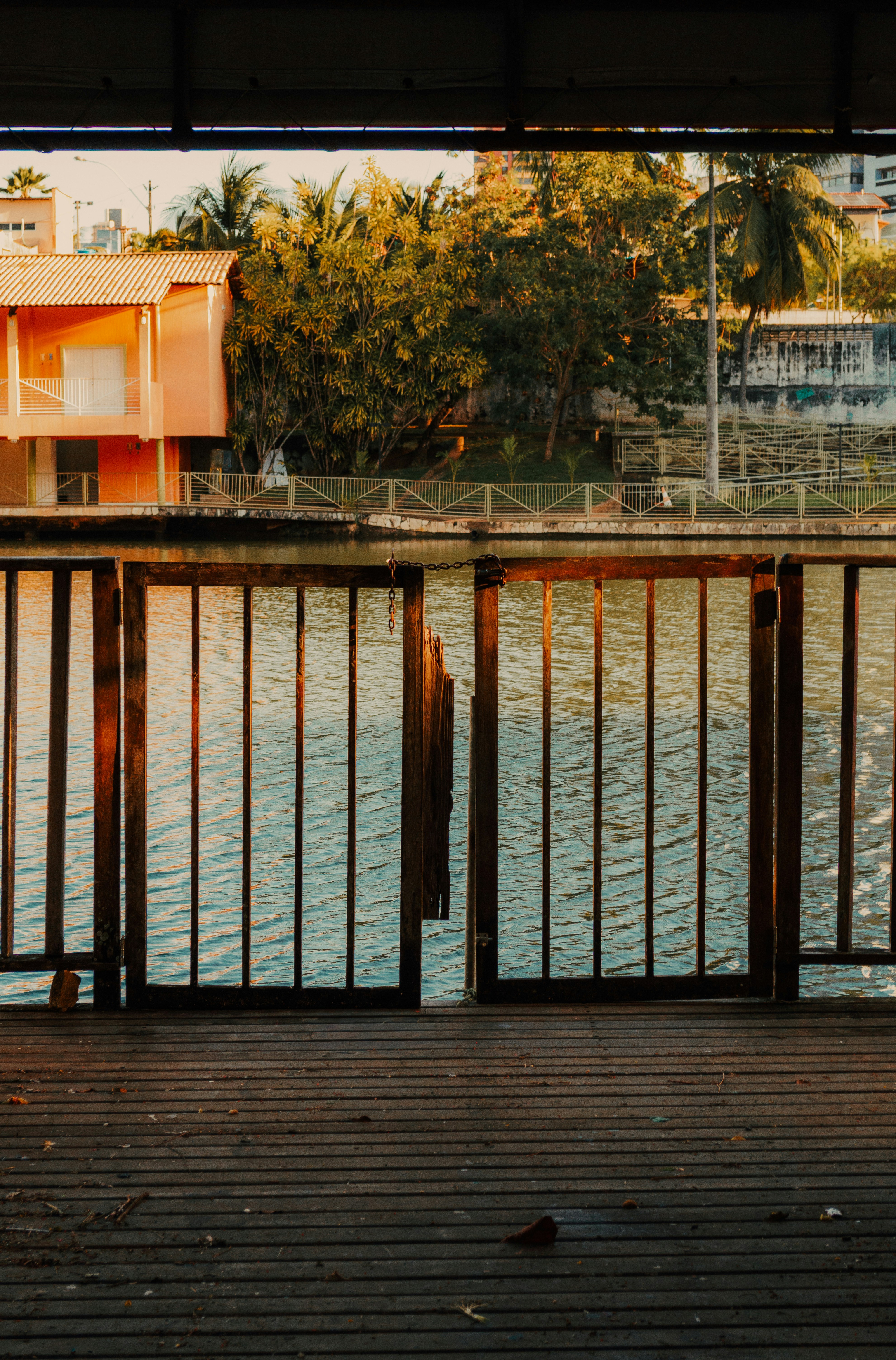 Wooden deck and metal railing overlooking water, buildings, and trees.