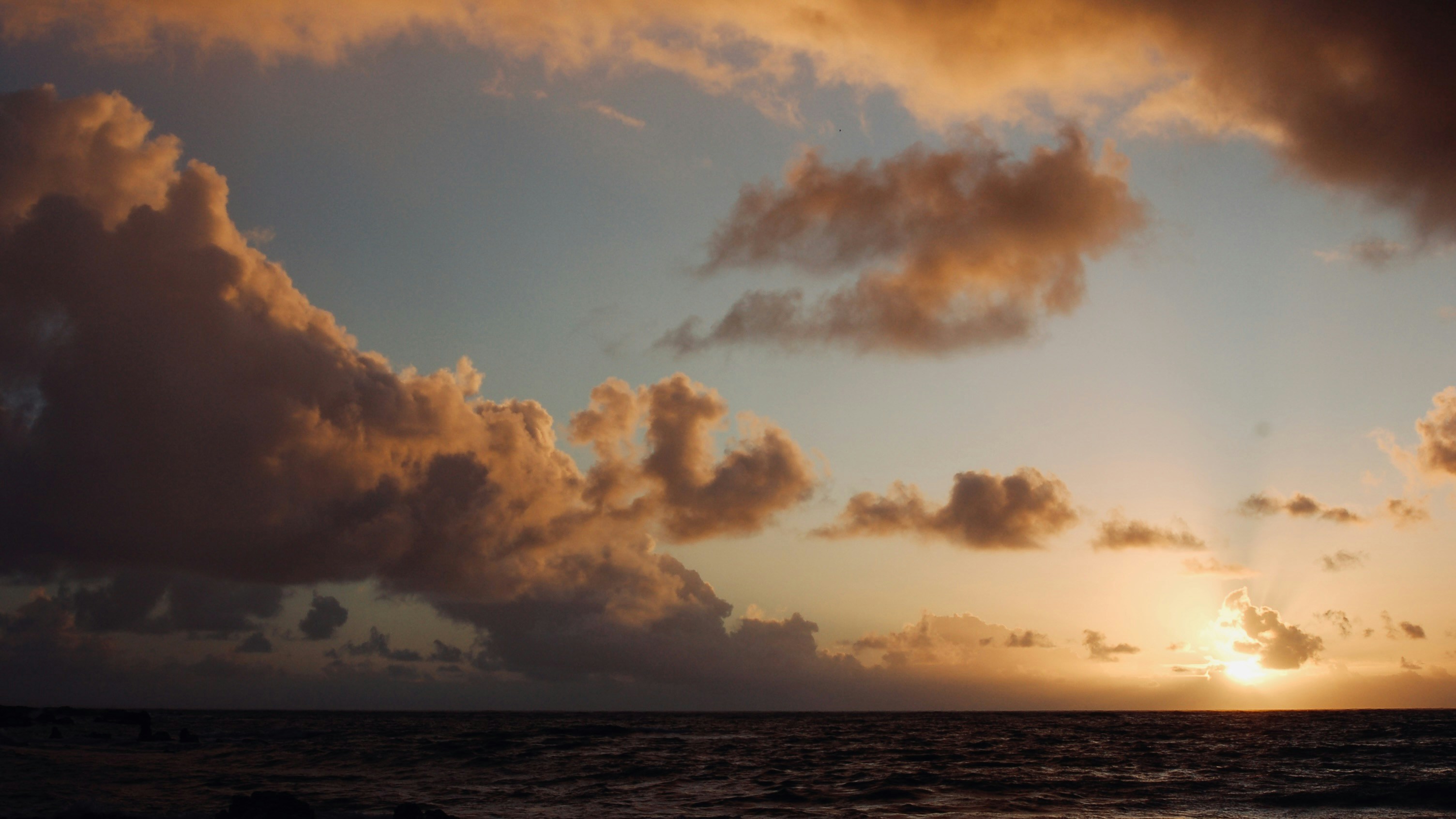 Vast ocean under a dramatic sunset with warm light on low-lying clouds; horizon line halves the frame, emphasizing calm water and glowing sky.