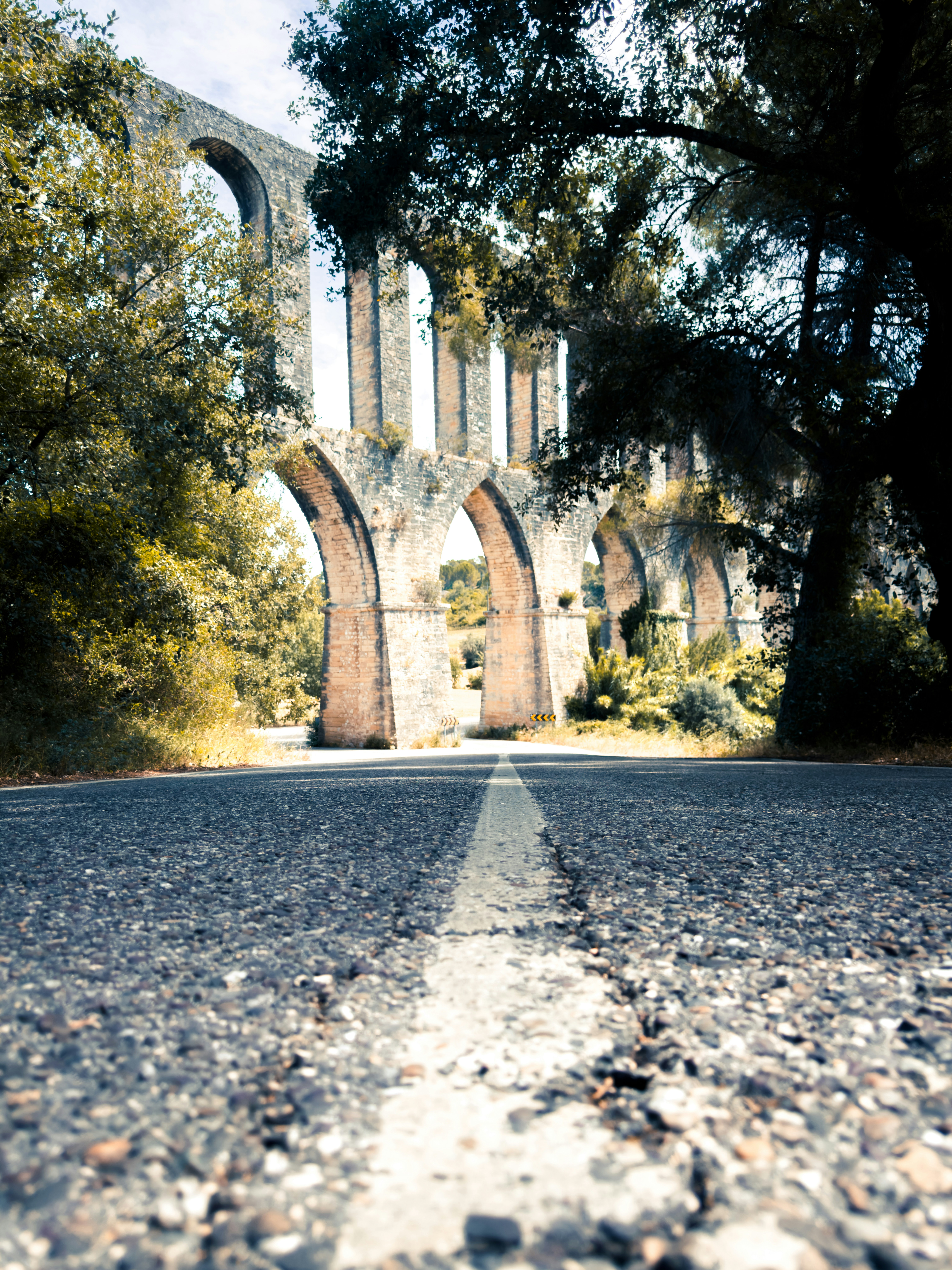Ancient aqueduct arches over a road with a white line.