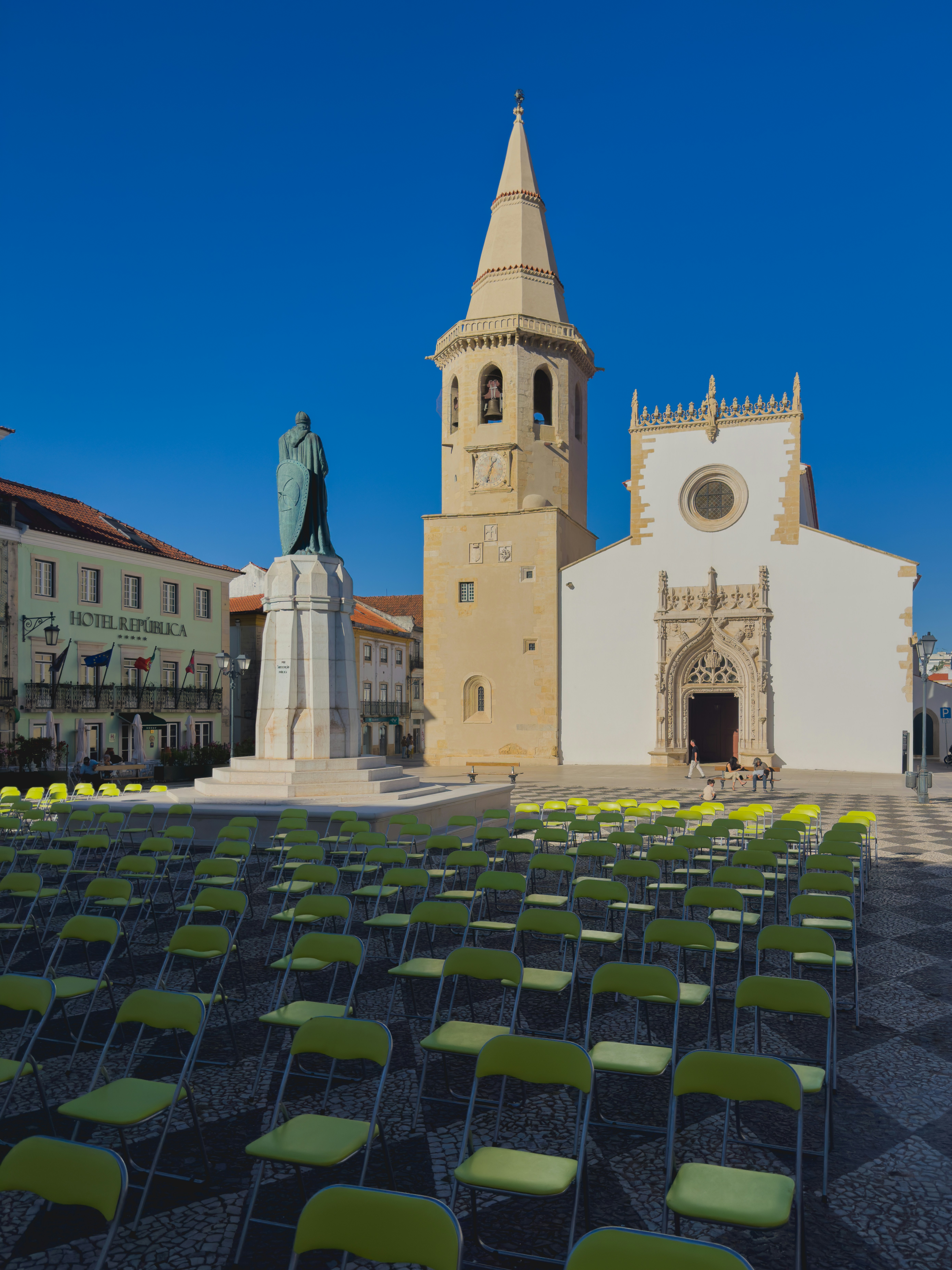 Sunlit Piazza: Historic Church, Clocktower, and Rows of Green Chairs