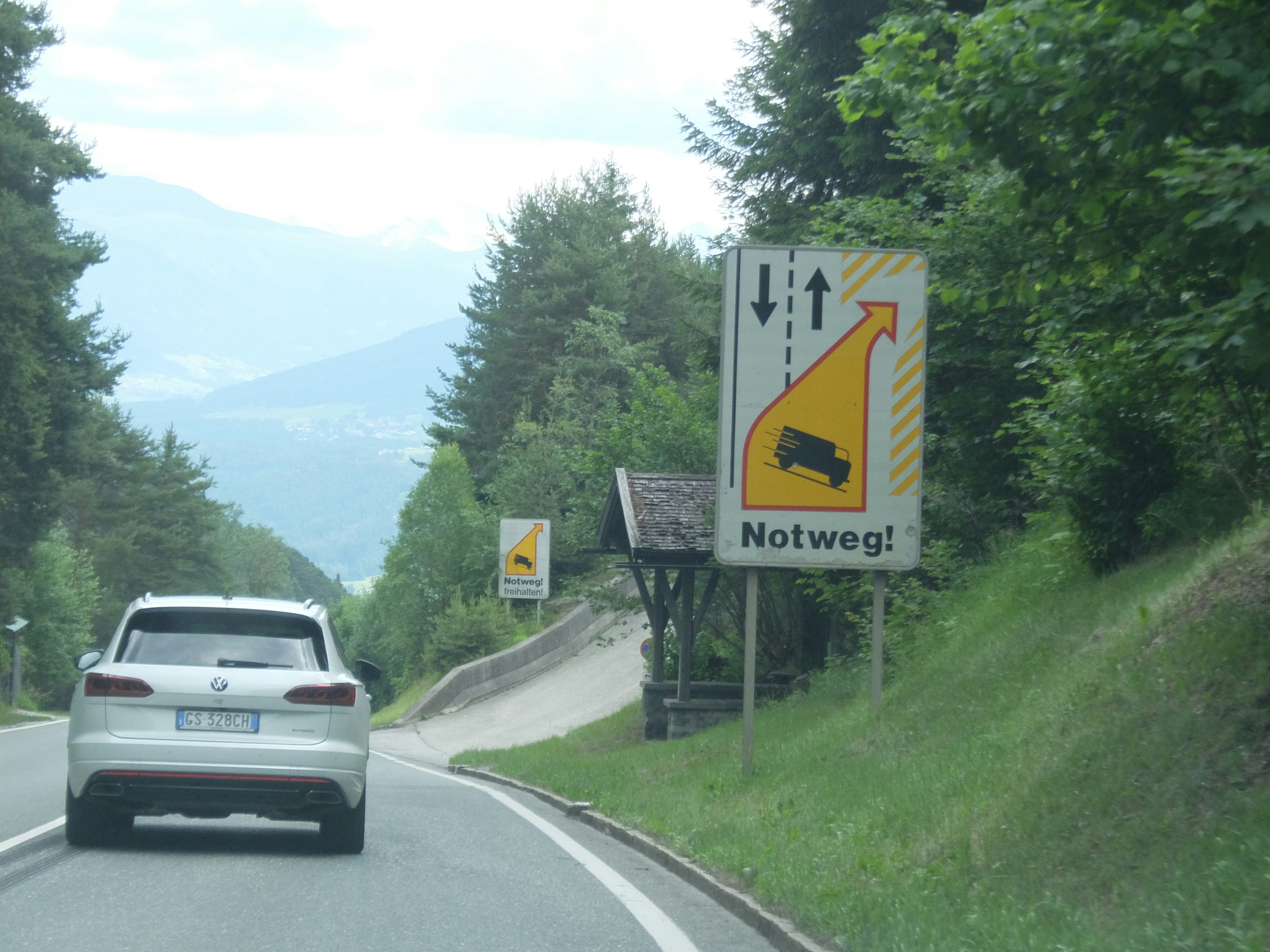 Signage on a Curved Mountain Road: A Quiet Drive Amid Forest and Distant Peaks