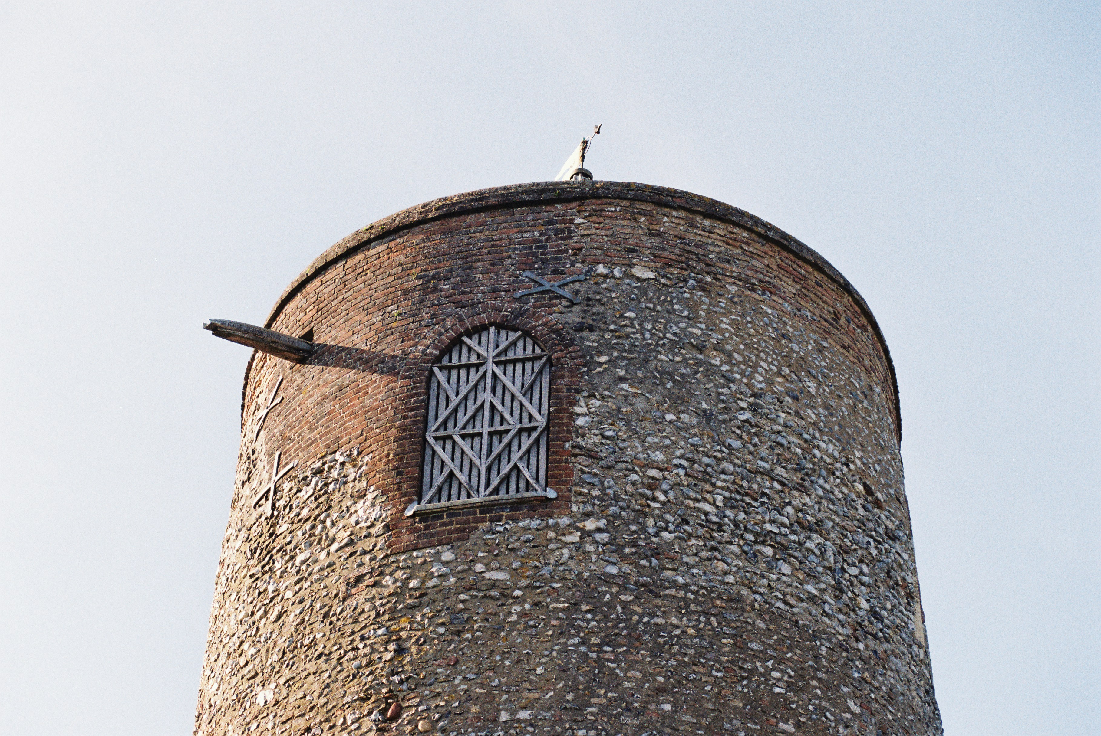 Circular stone tower with a small lattice window and a protruding beam set against a pale sky.