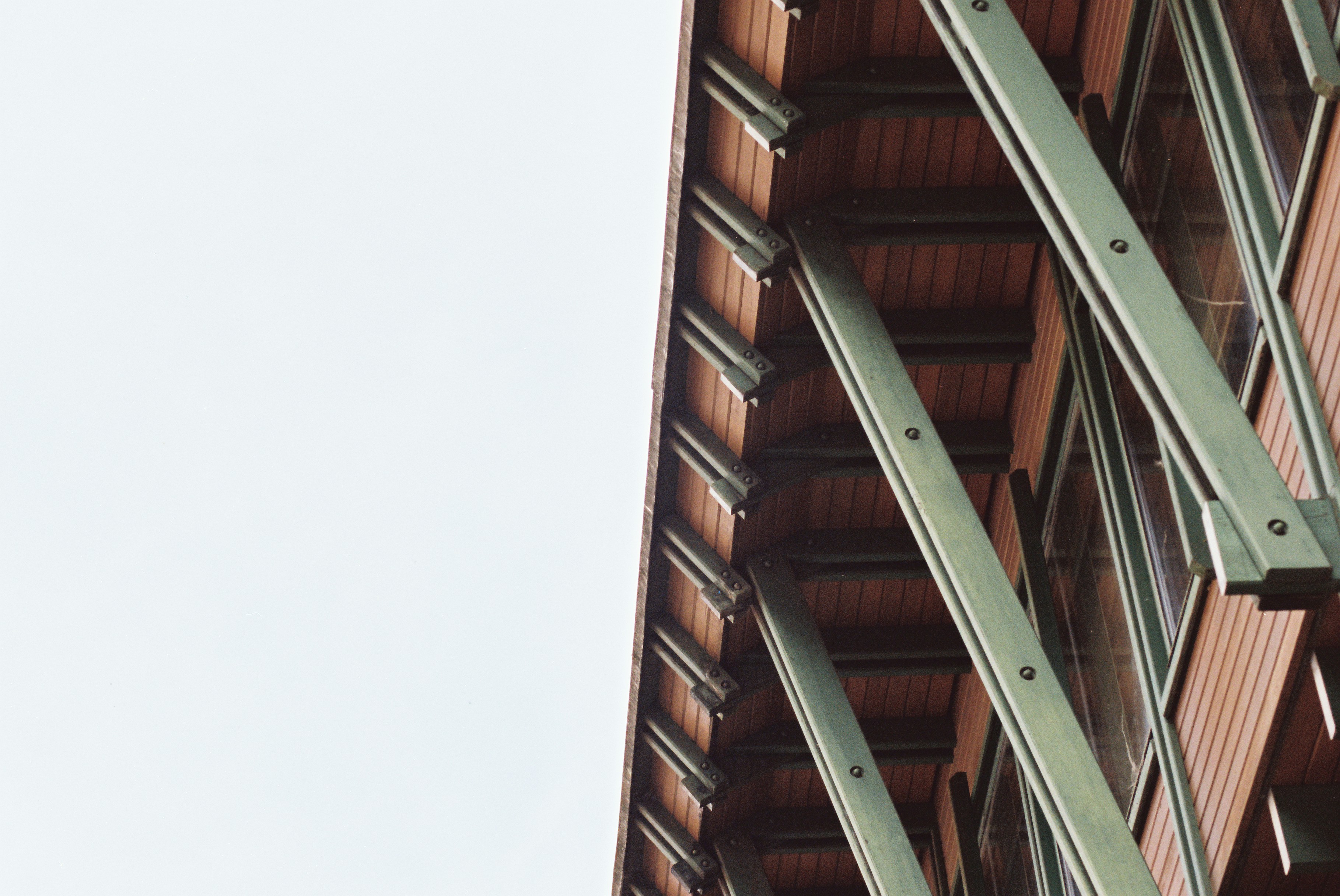 Close-up of green-painted steel supports and wooden beams forming a structural pattern against a pale sky; the image highlights industrial architecture details. This is a photograph of structural elements.