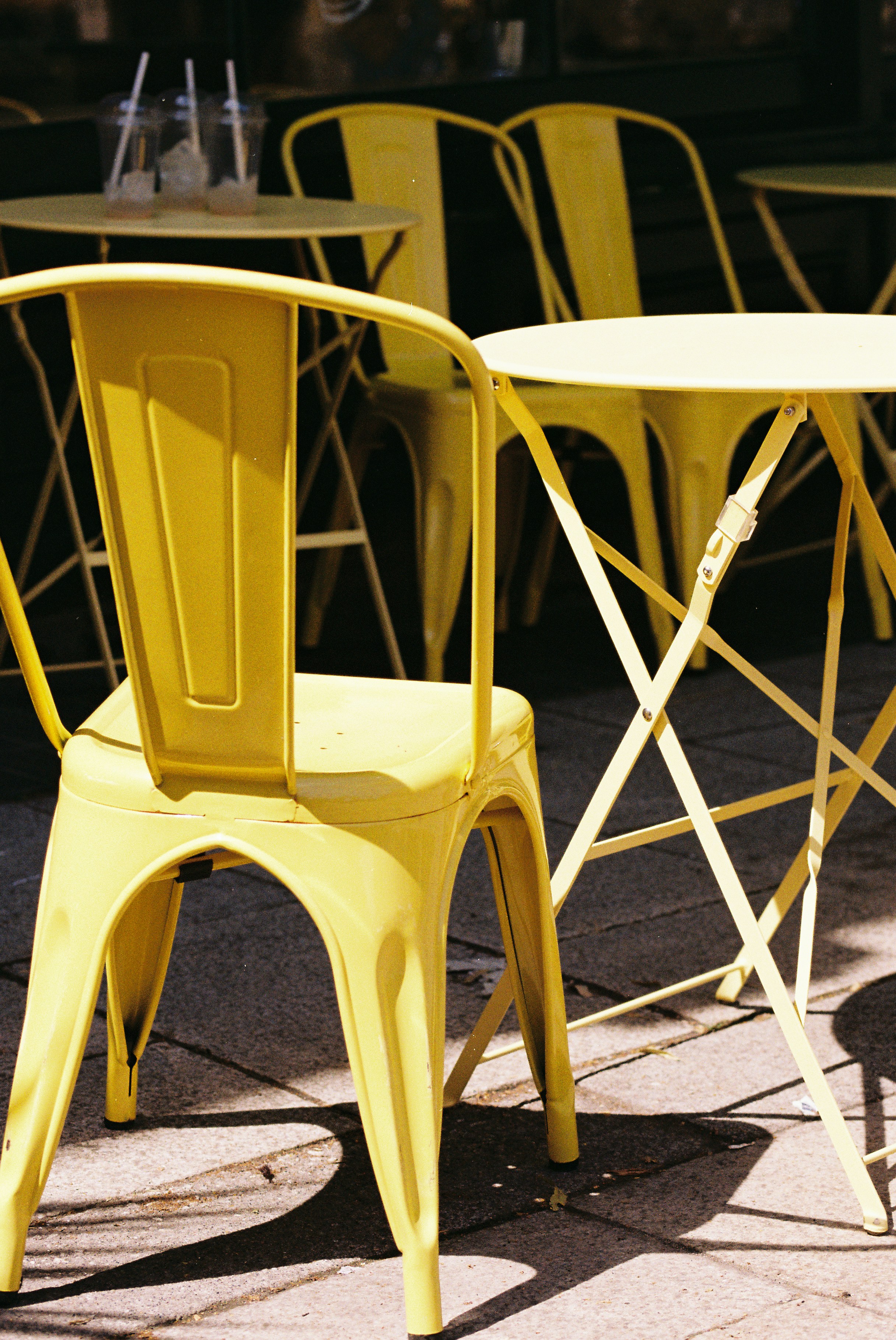 Bright yellow metal cafe chairs and tables catch warm sunlight on a city pavement.