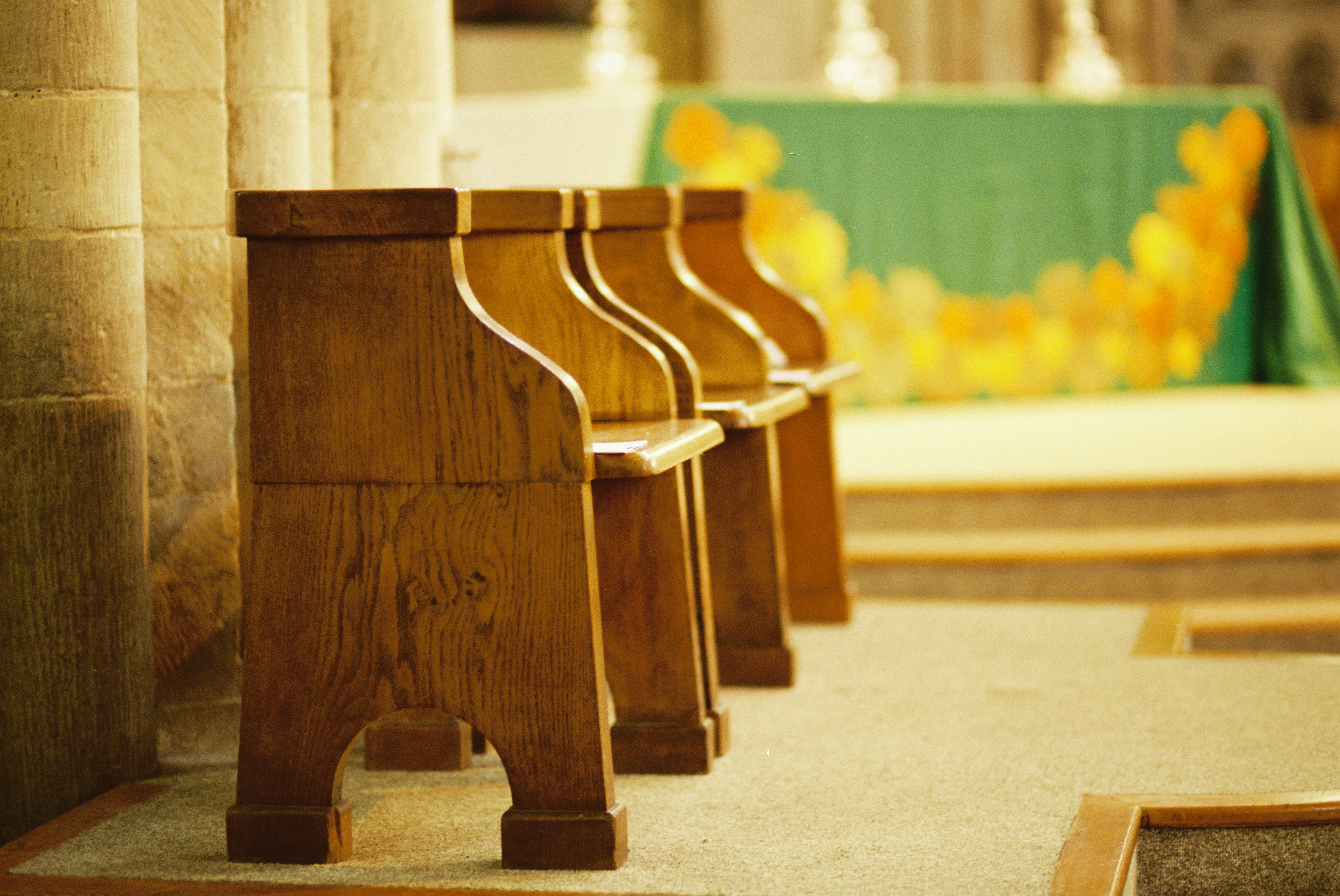 Carved oak choir stalls stand beside a green altar cloth edged with yellow flowers in soft light.