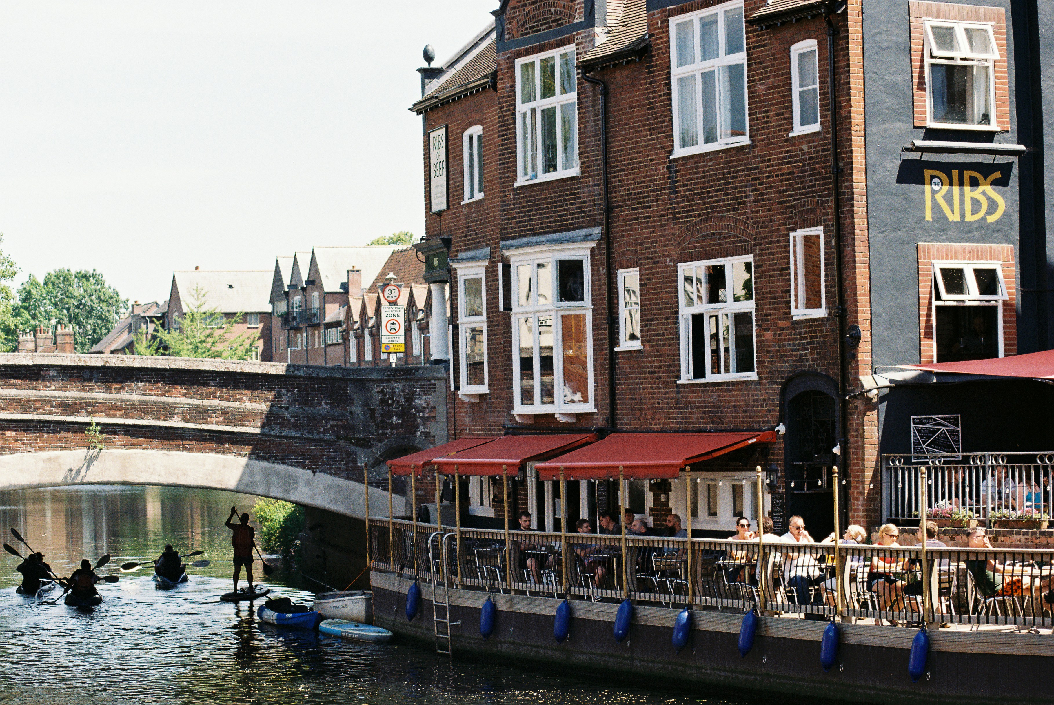 Riverside Café Proscenium: Brick Facades, Outdoor Tables, and a Quiet Canopy of Light