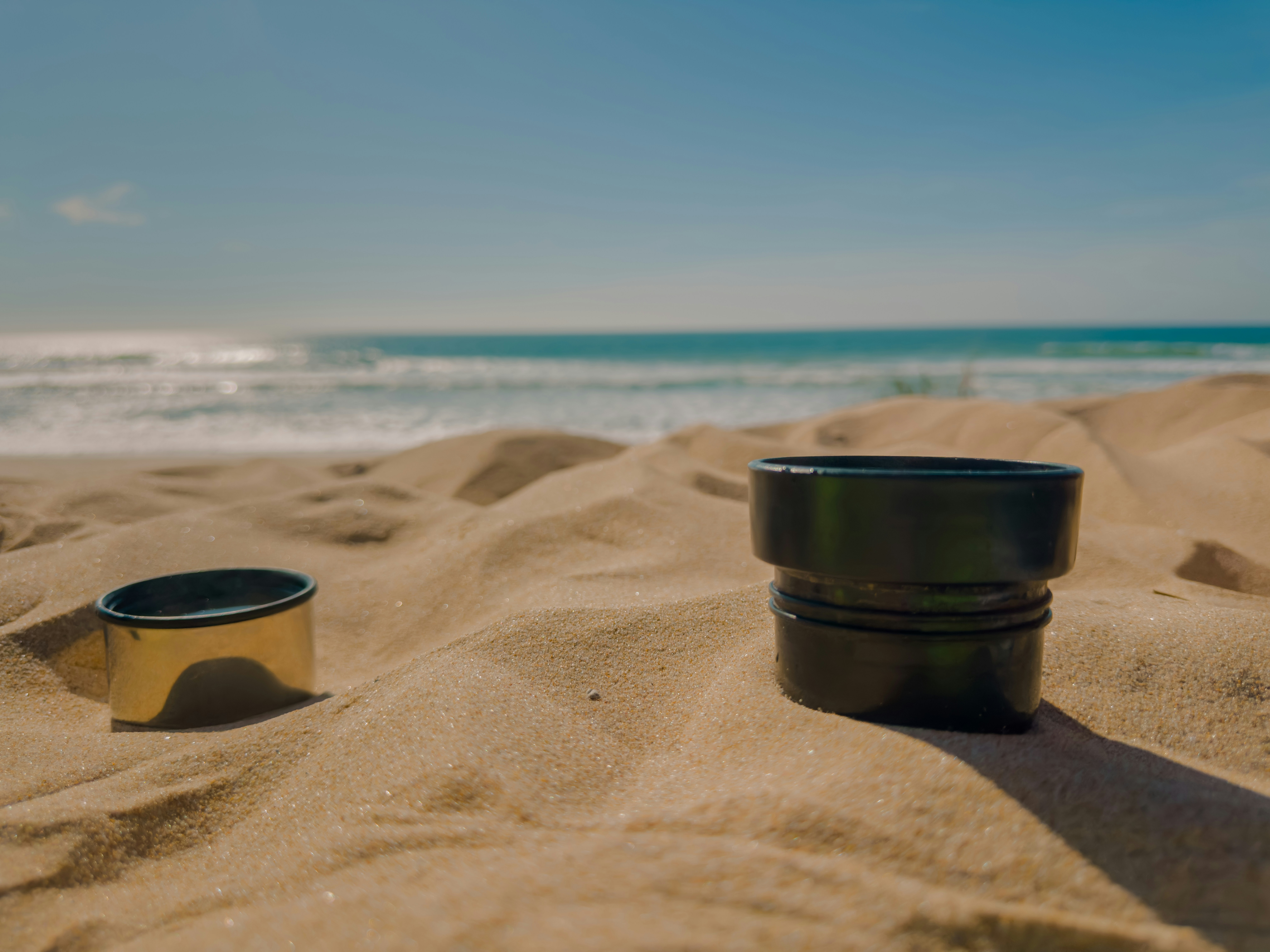 Two Camera Lids Resting on Golden Sand at the Shore
