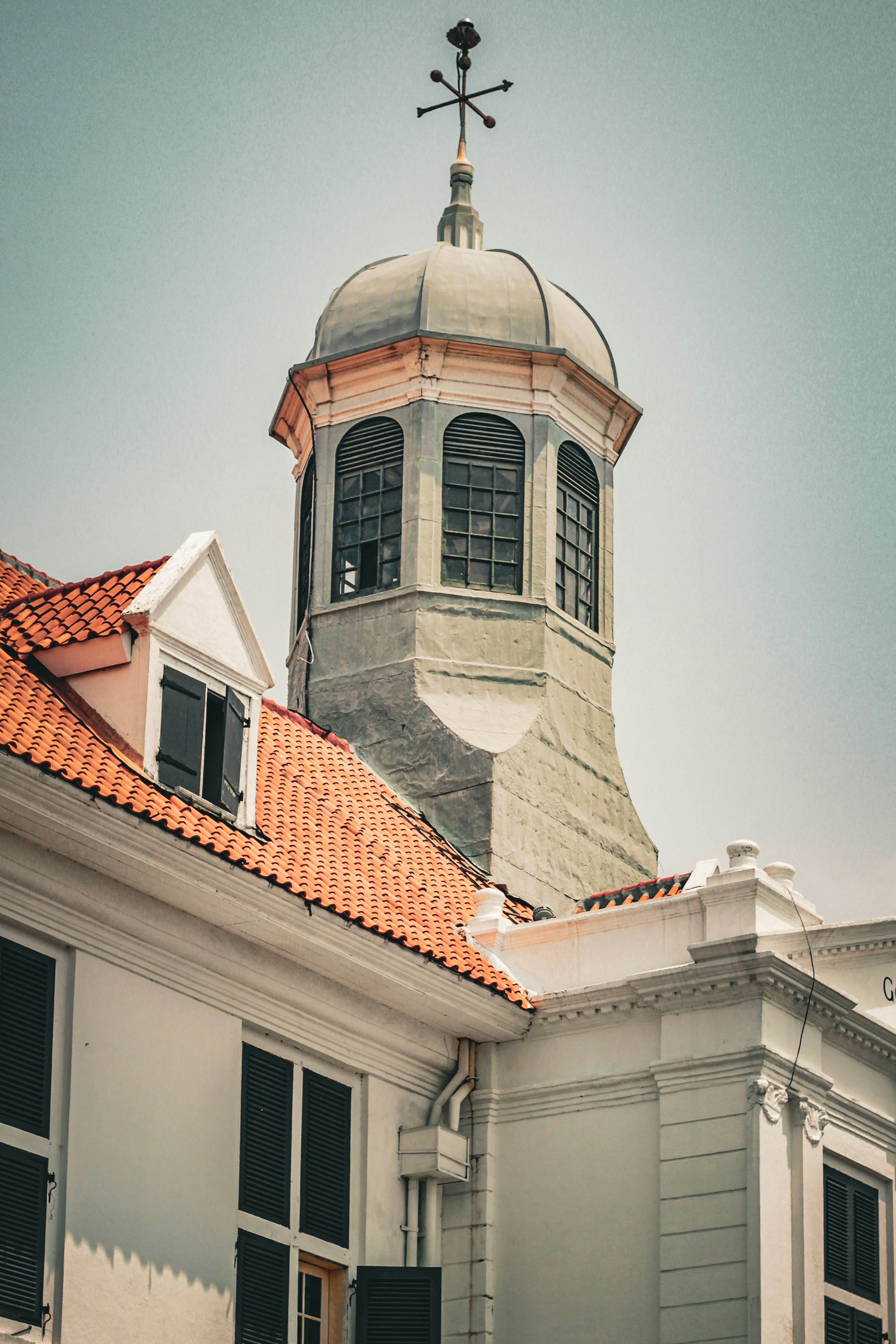 Architectural tower with a domed cupola and arched windows rises above white walls and red tiles. A classic urban rooftop scene emphasizing the vertical landmark.