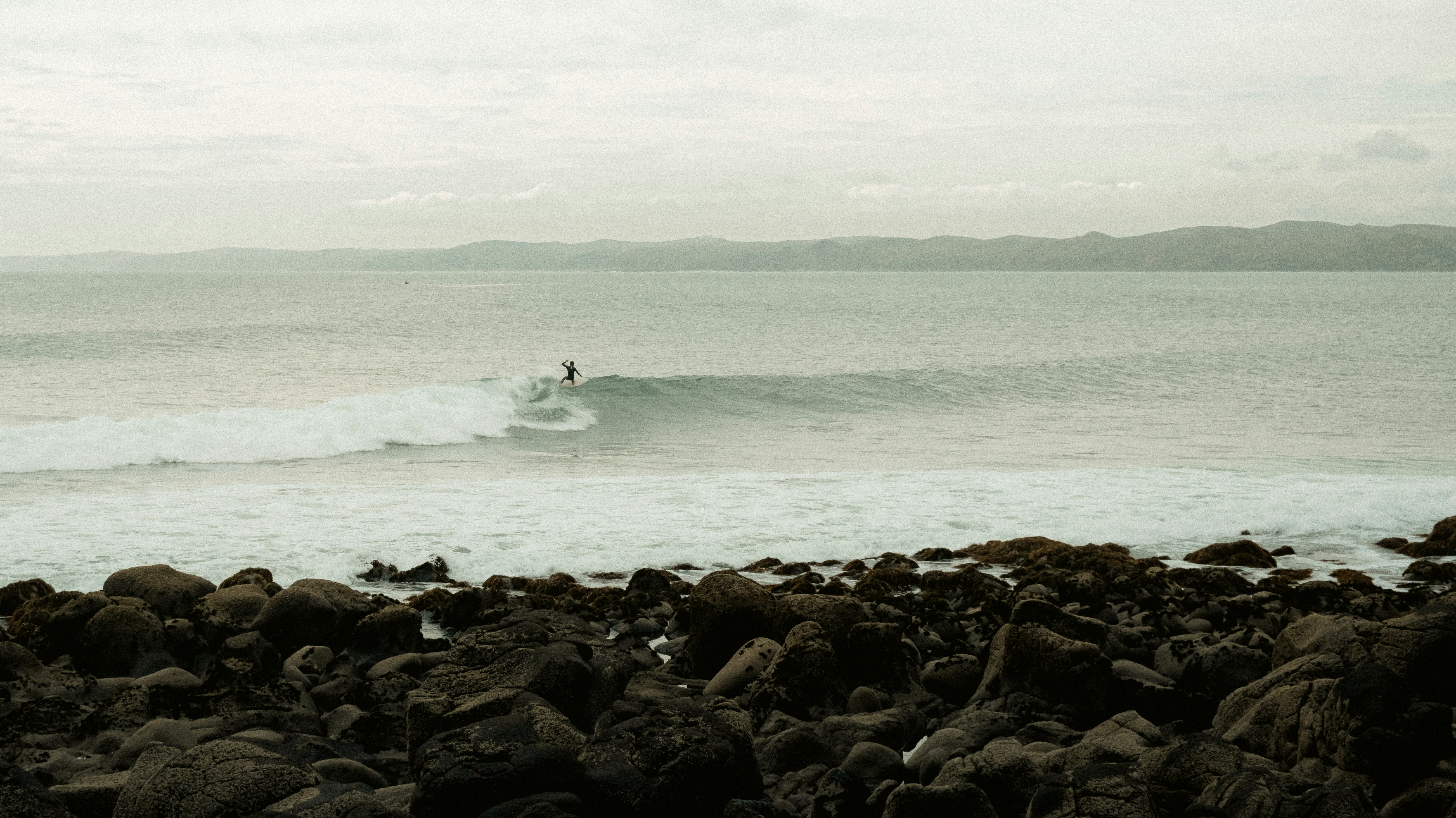 Lonely Surfer riding a distant crest on a misty morning