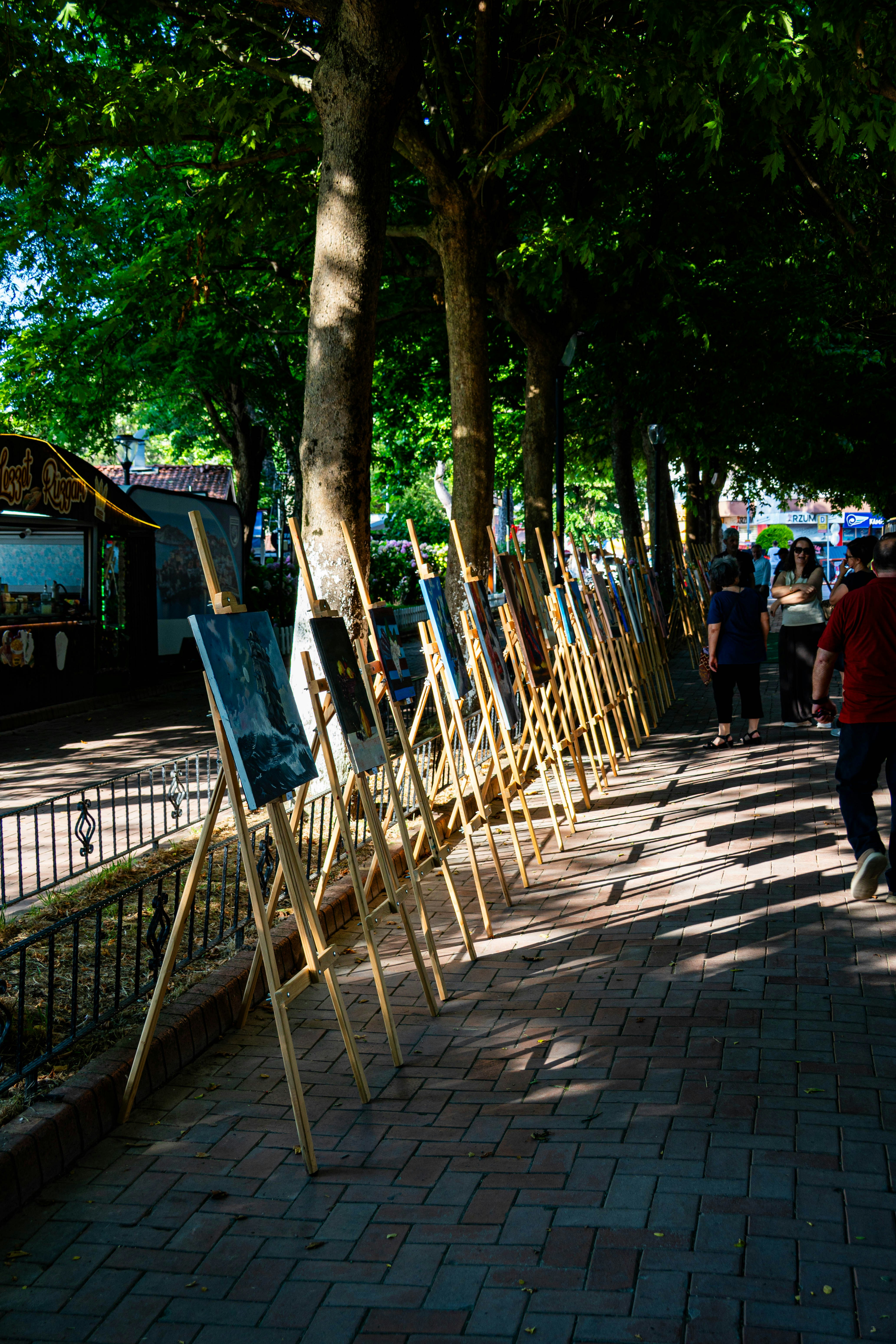 Row of Easel Paintings Along a Shaded City Path