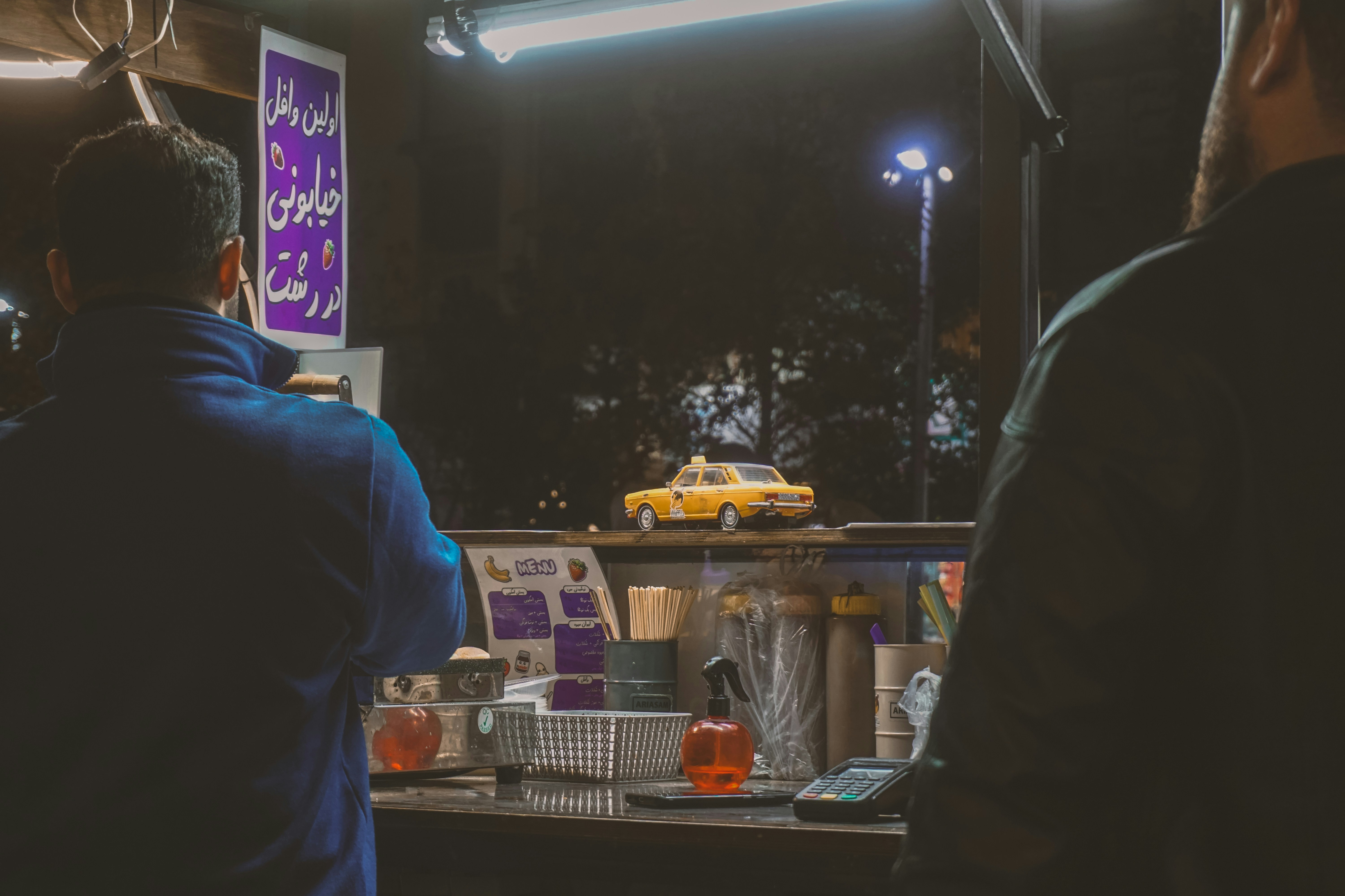 Night kiosk glow: a yellow taxi paused beyond the counter edge
