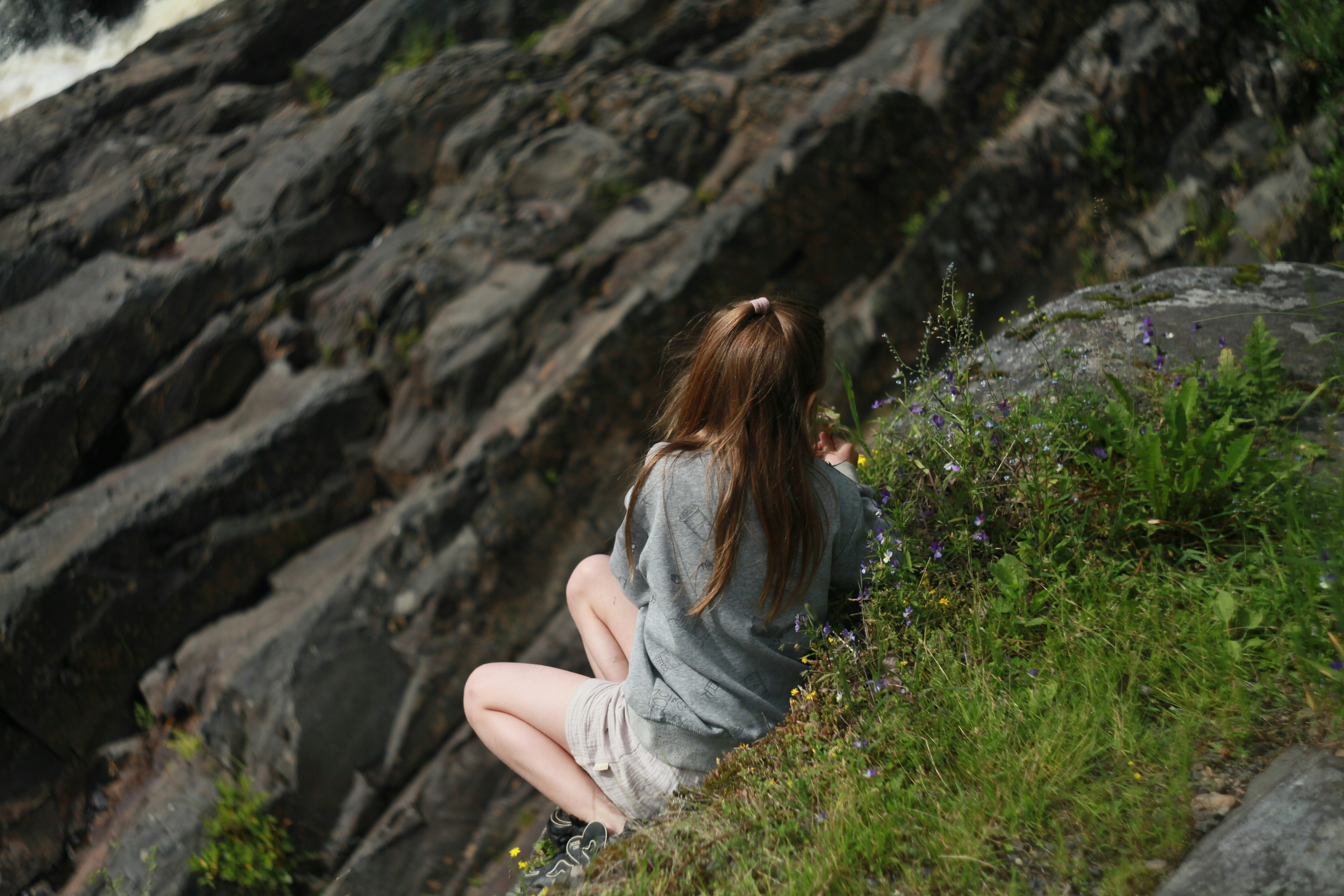 Quiet Pause on the Cliff: A Seated Figure Among Wildflowers
