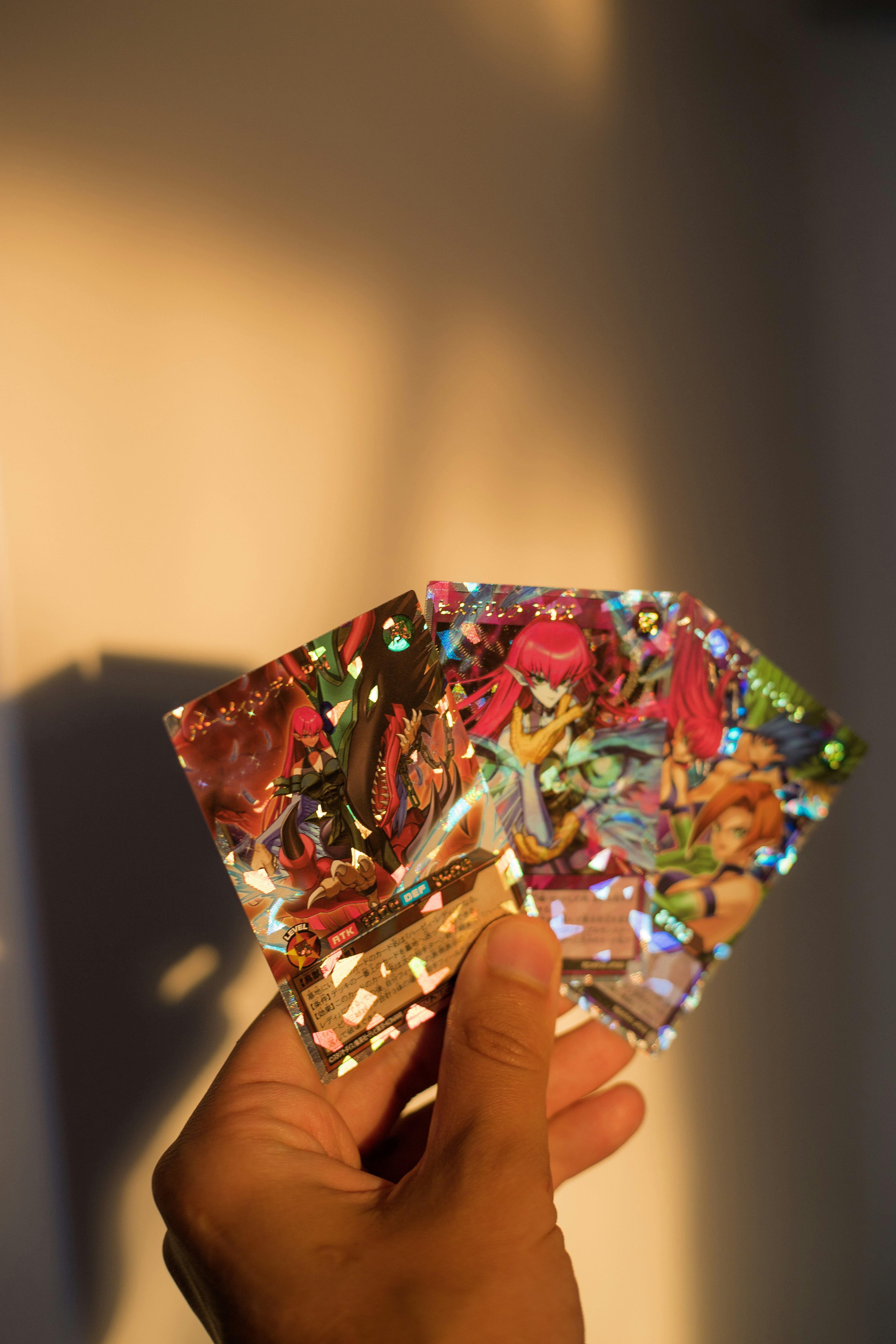 Colorful trading cards held by a hand against a warm, blurred background; a logo-printed, glossy set fanned in the foreground.