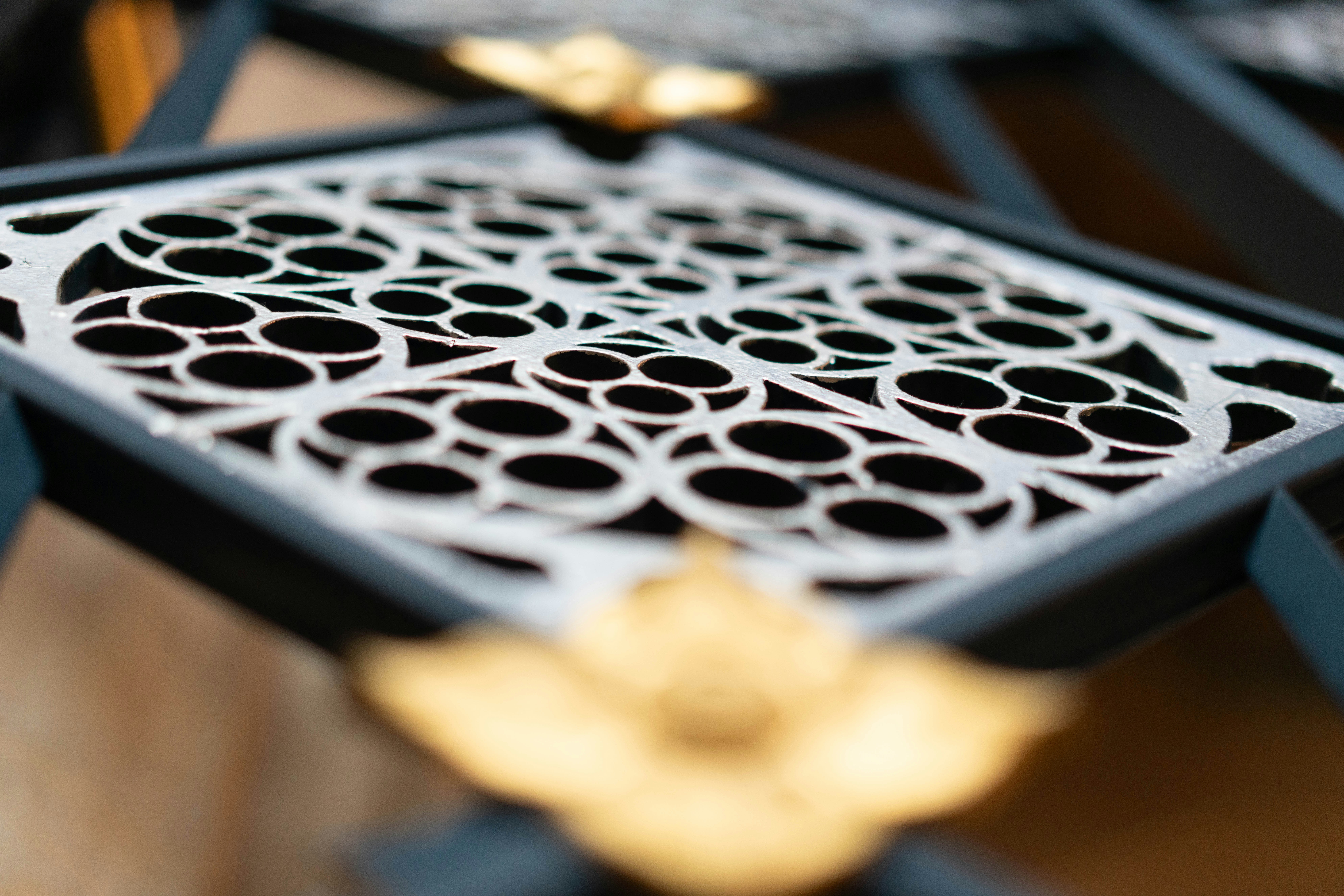 Close-up of a circular metal grate with repeating rings, blurred foreground leaves, and shallow depth of field. A decorative industrial detail captured for texture and pattern.