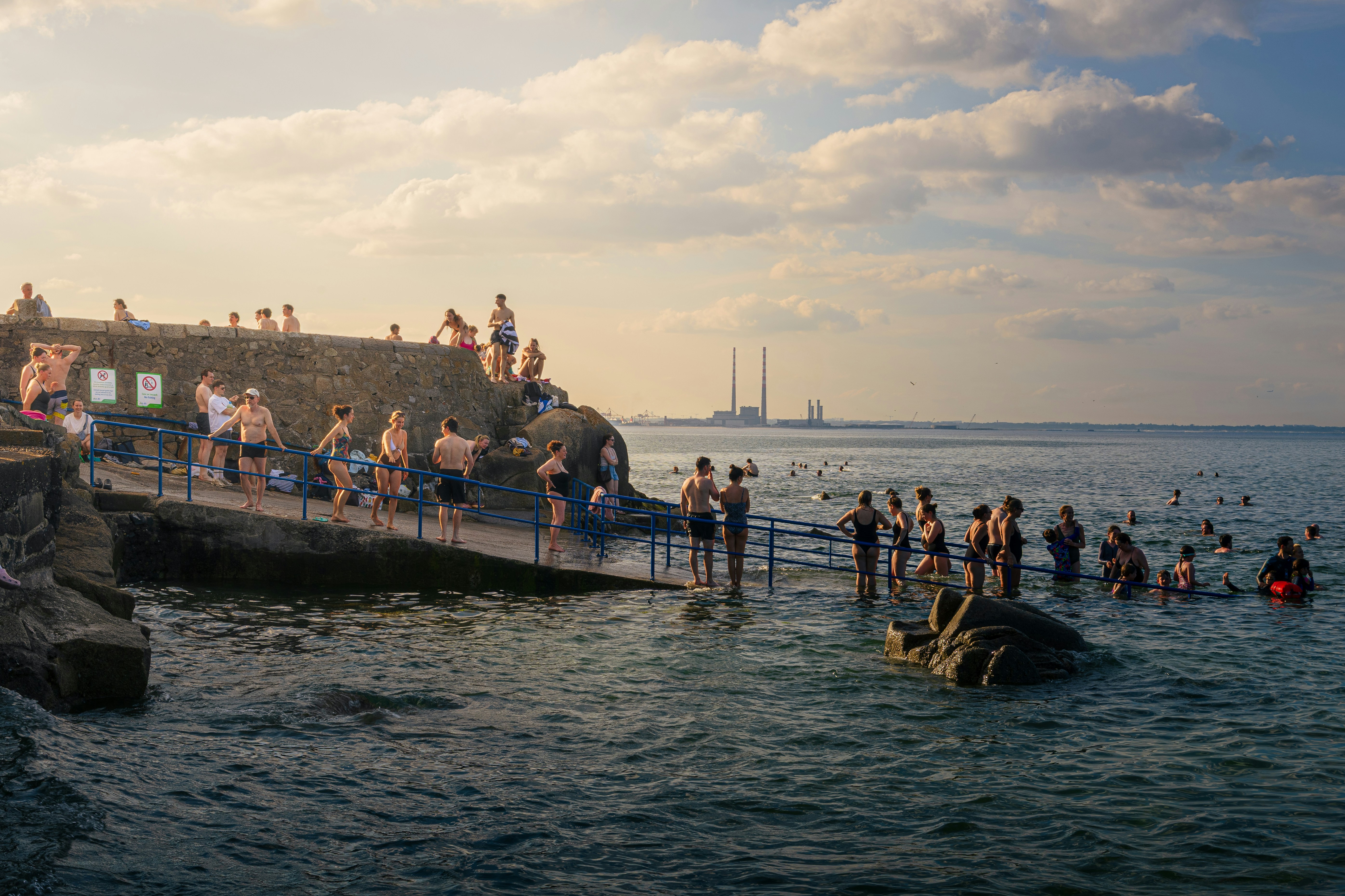 People at a seaside jetty bathed in warm late-afternoon light