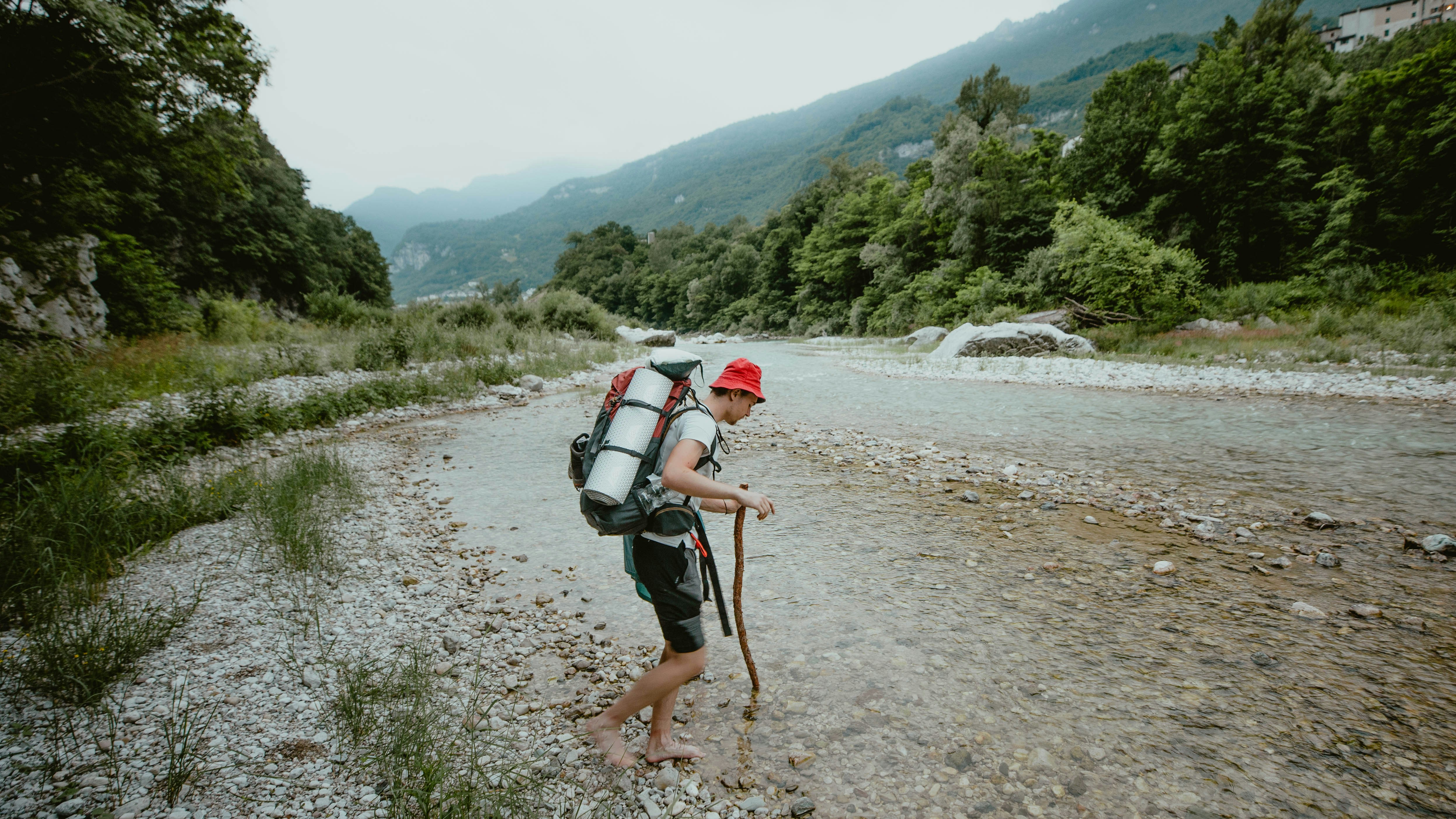 Climber with a Grail of Gear Crossing a Pebble River
