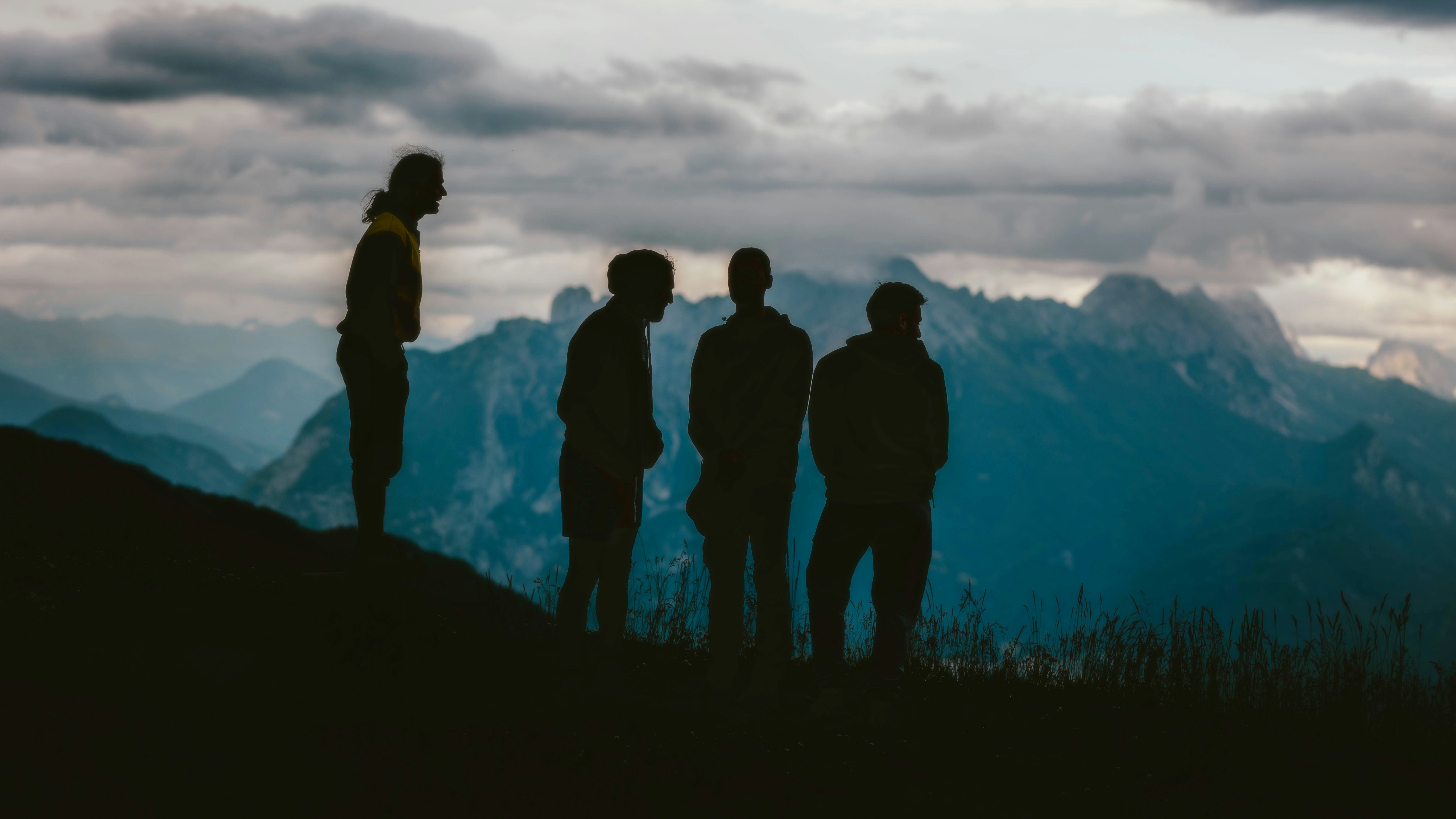 Four silhouettes on a ridge as alpine peaks glow at dusk