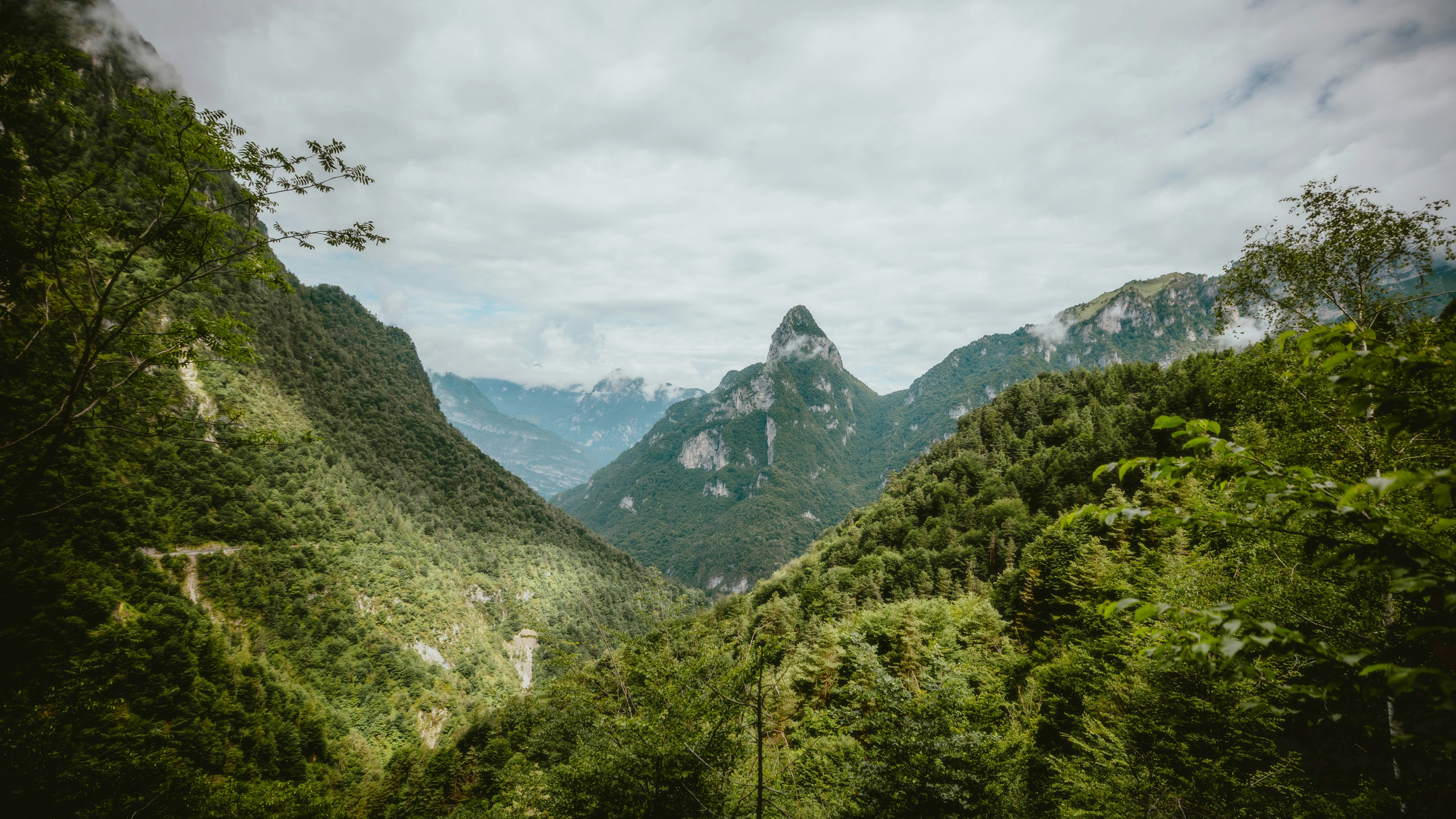 Verdant mountain valley with a towering peak and cloudy skies.