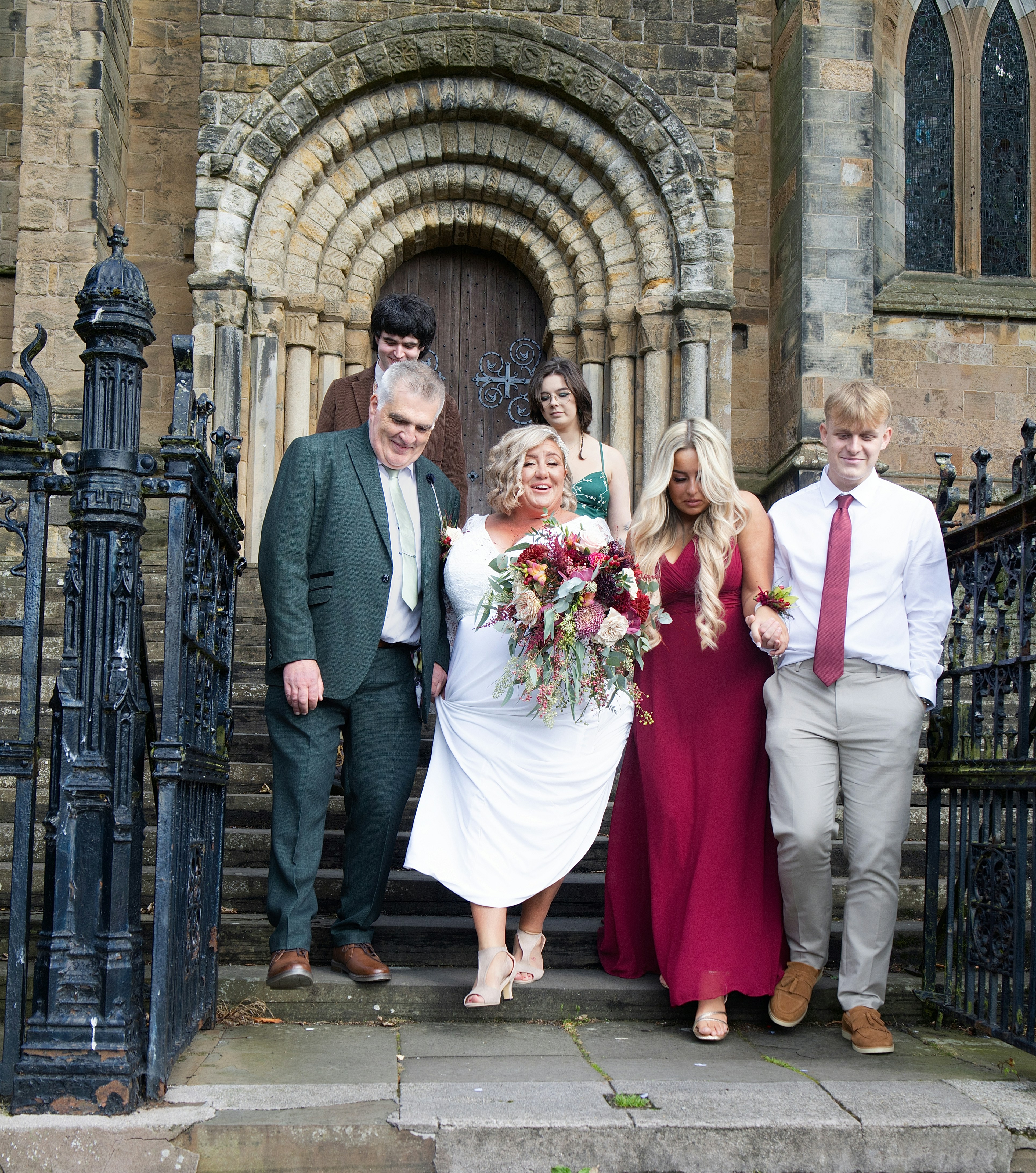 A joyful wedding party exits a stone church building.