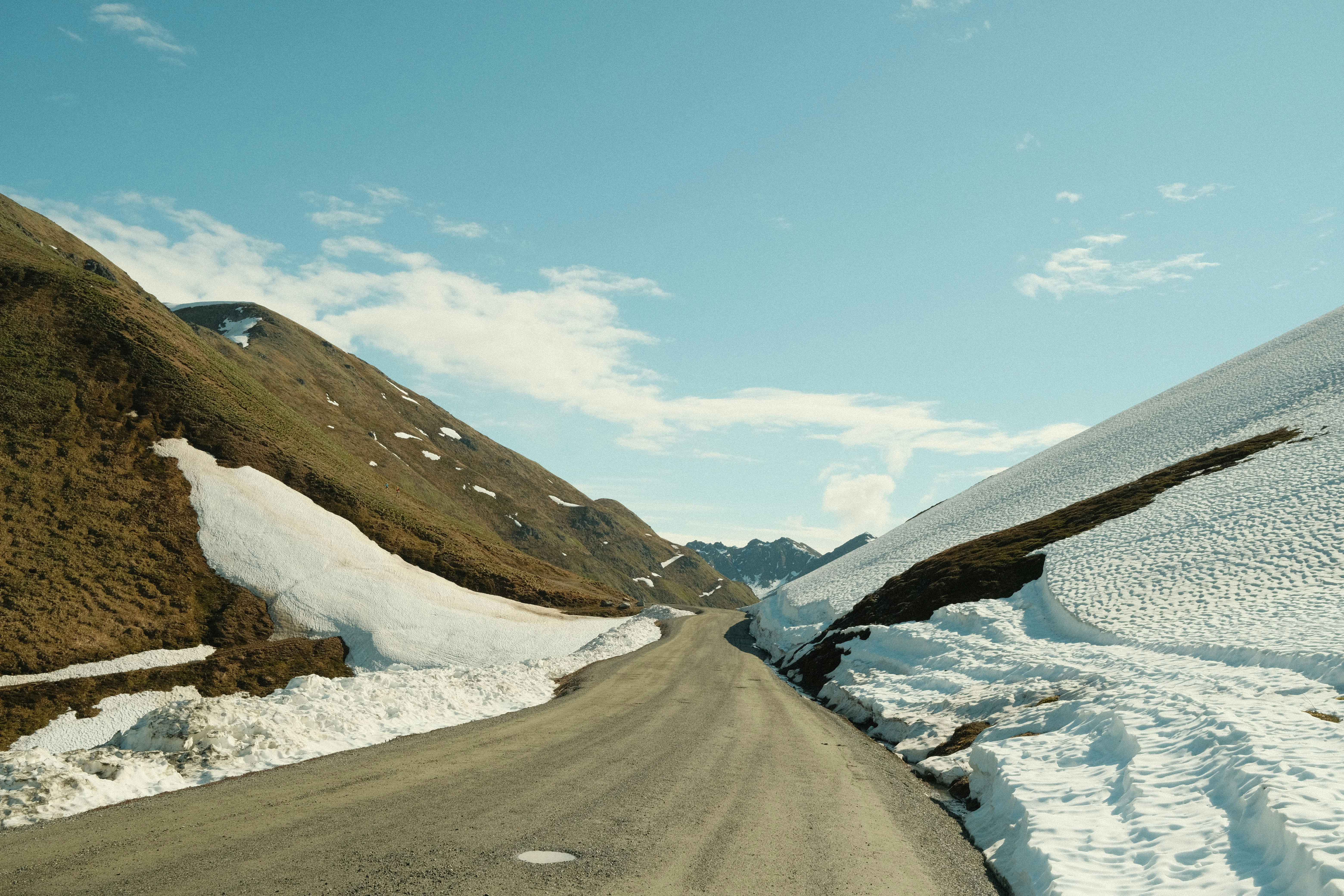a gravel road leads between a snowy mountain pass