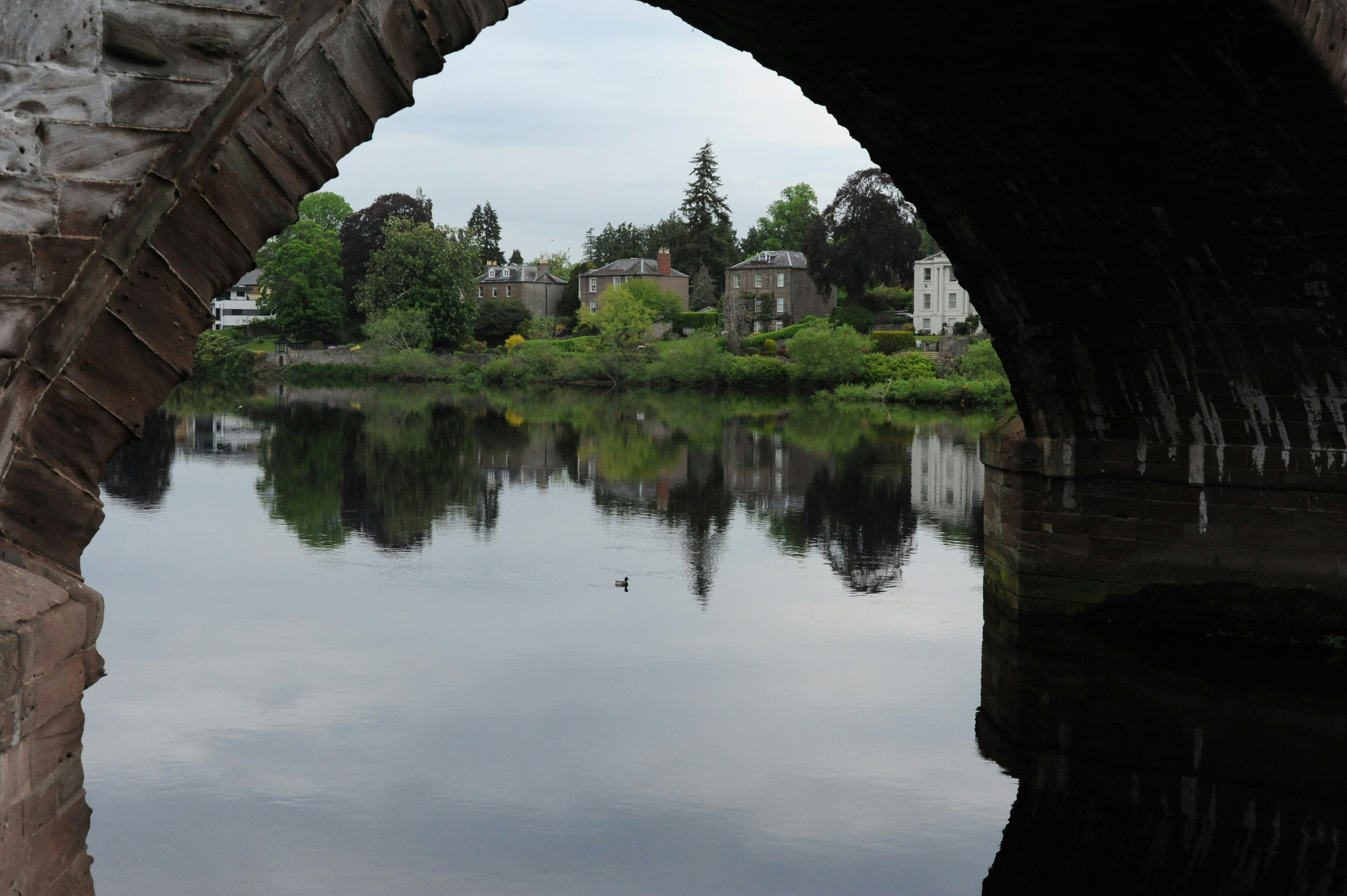 Through the Stone Arch: Riverside Village Framed by a Darkened Bridge