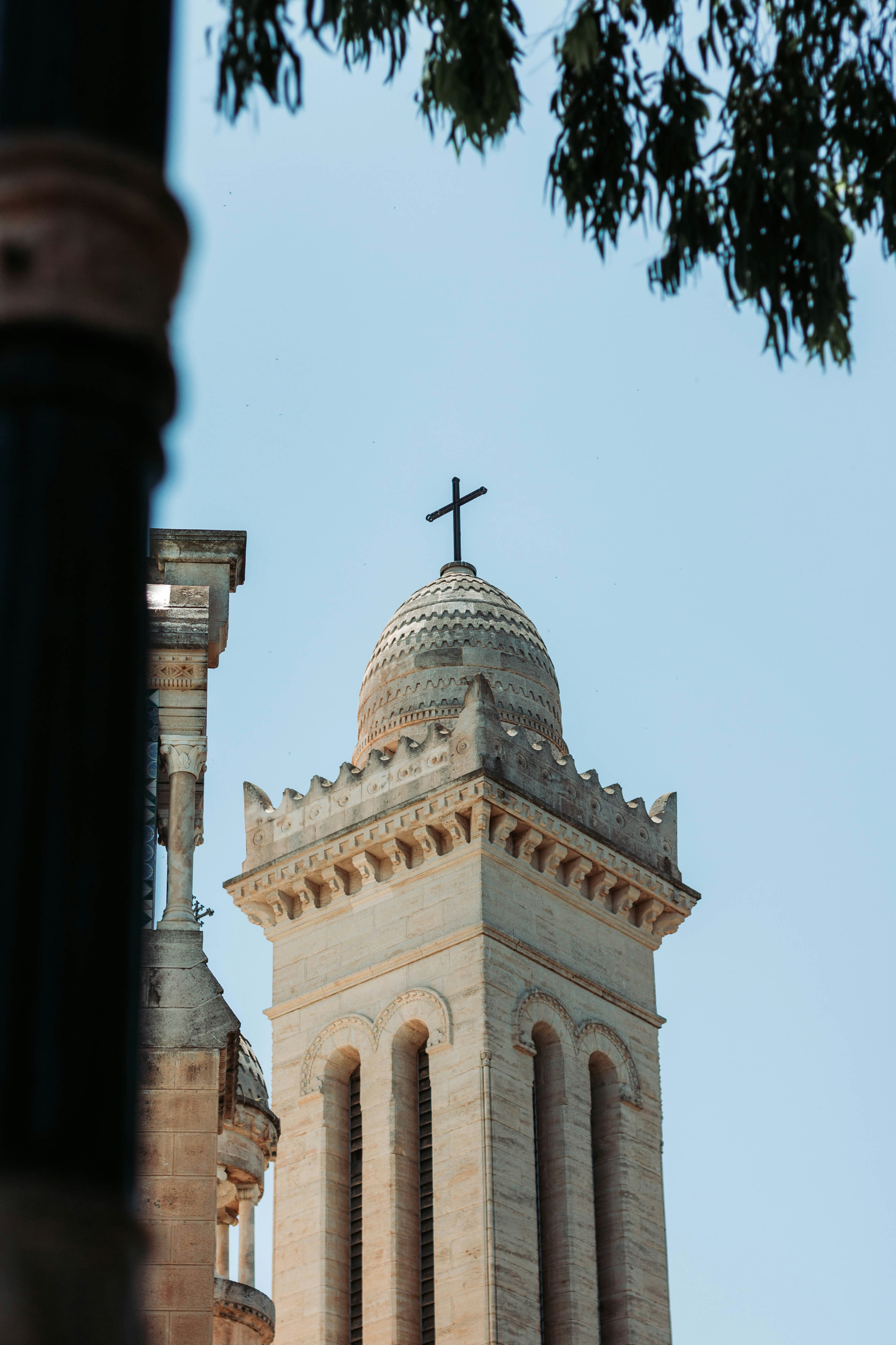 Cross atop a Romanesque tower under a calm blue sky