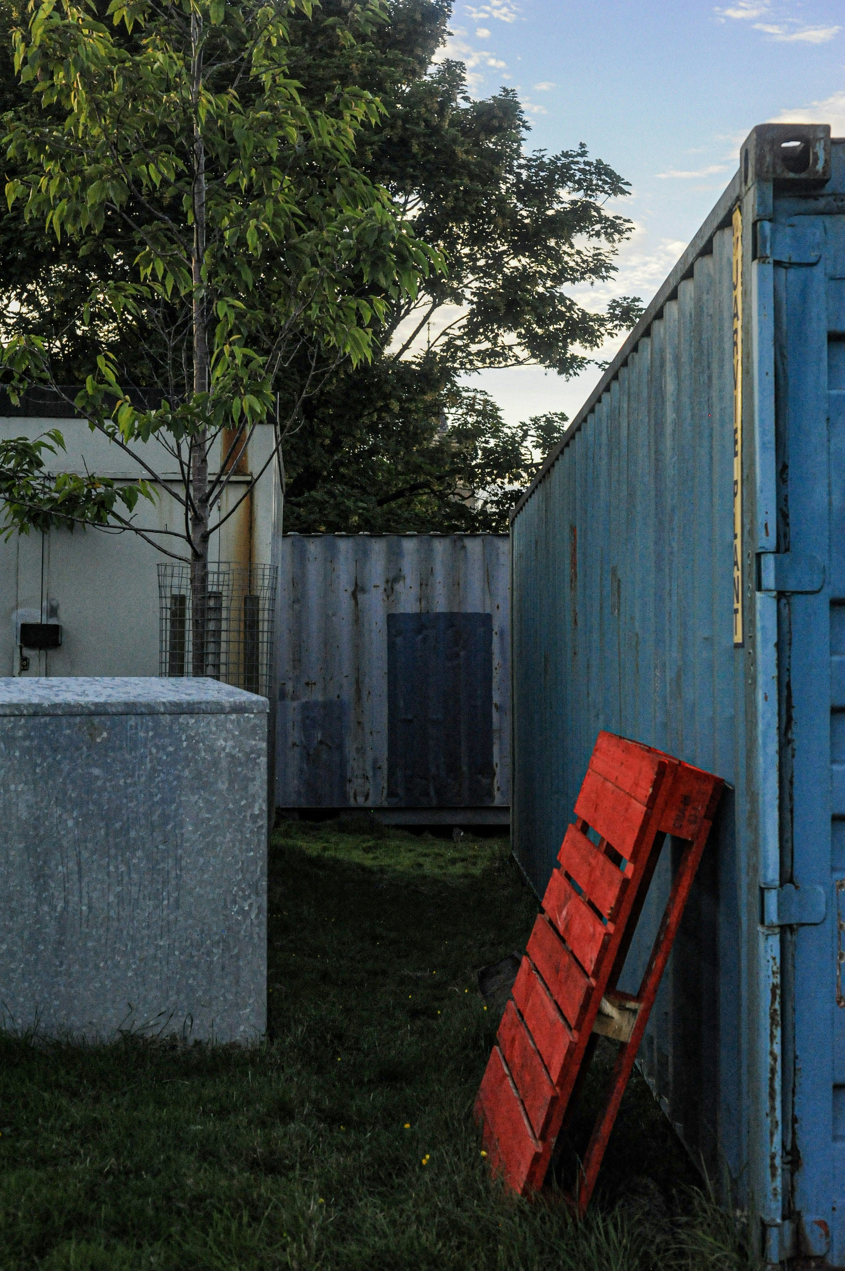Red Slatted Lean-to: A Quiet Alley Between Blue Containers