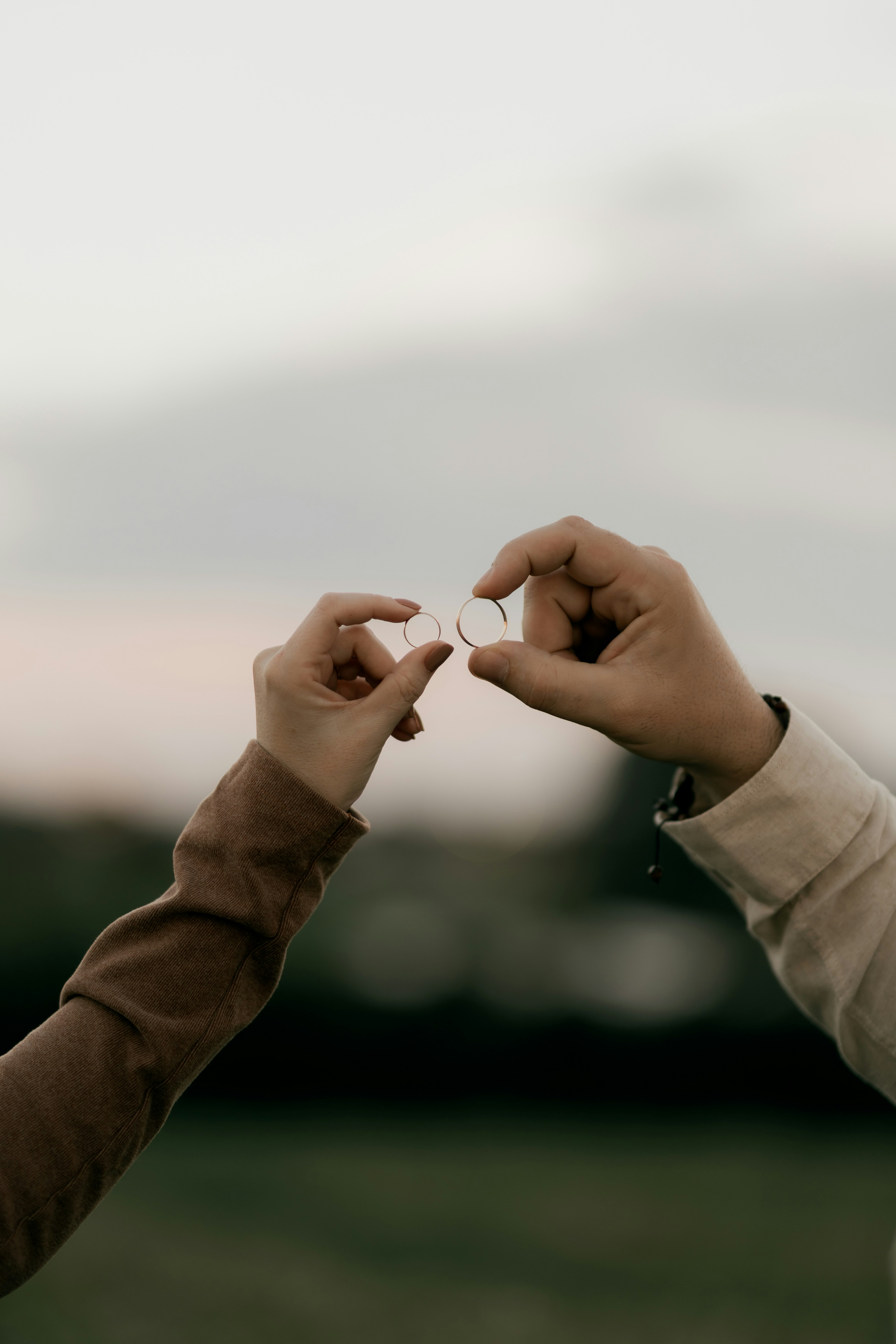 Two delicate rings held by intertwined fingers at sunset