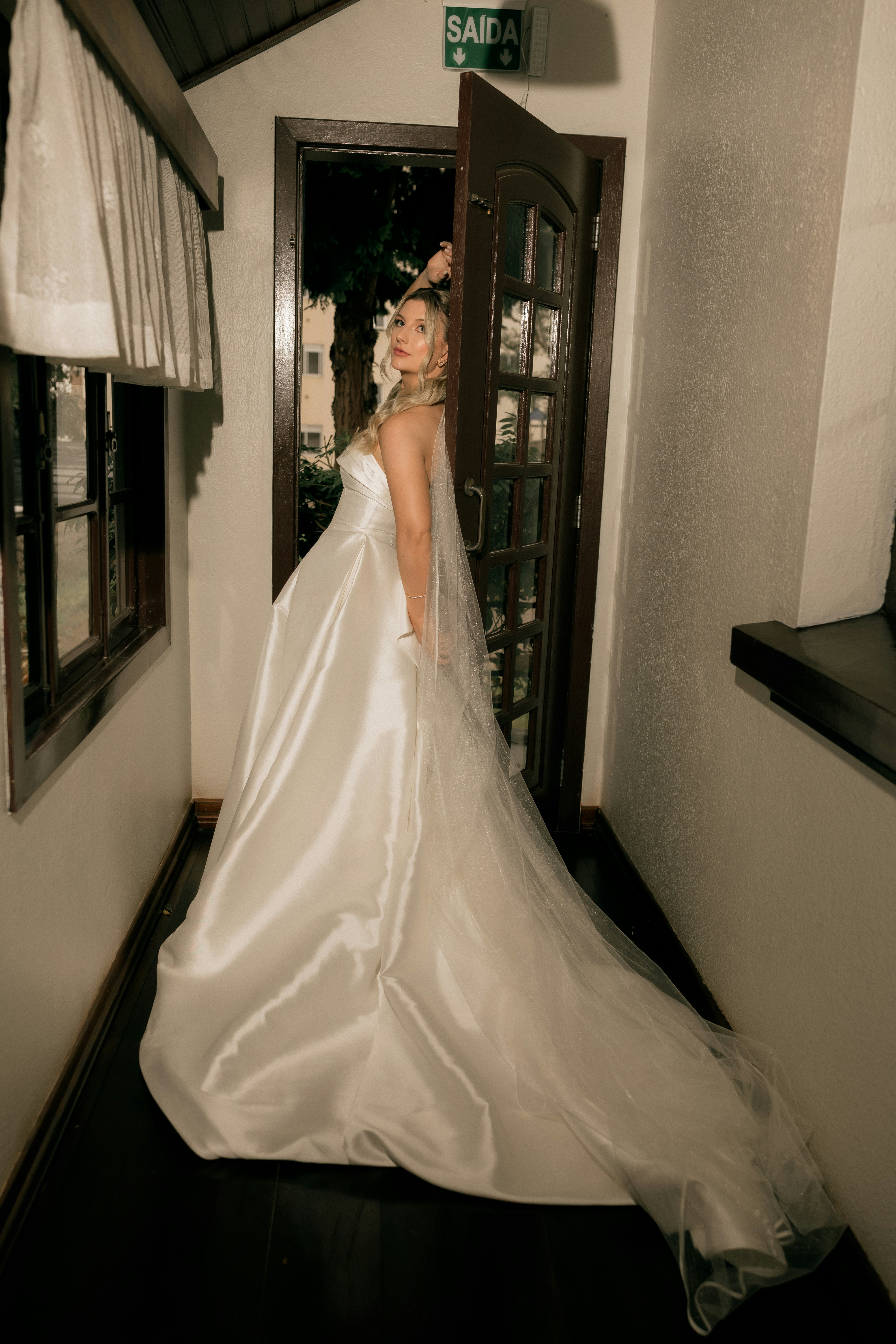 Veiled Exit: Bride in a Sunlit Hallway Steps into the Open