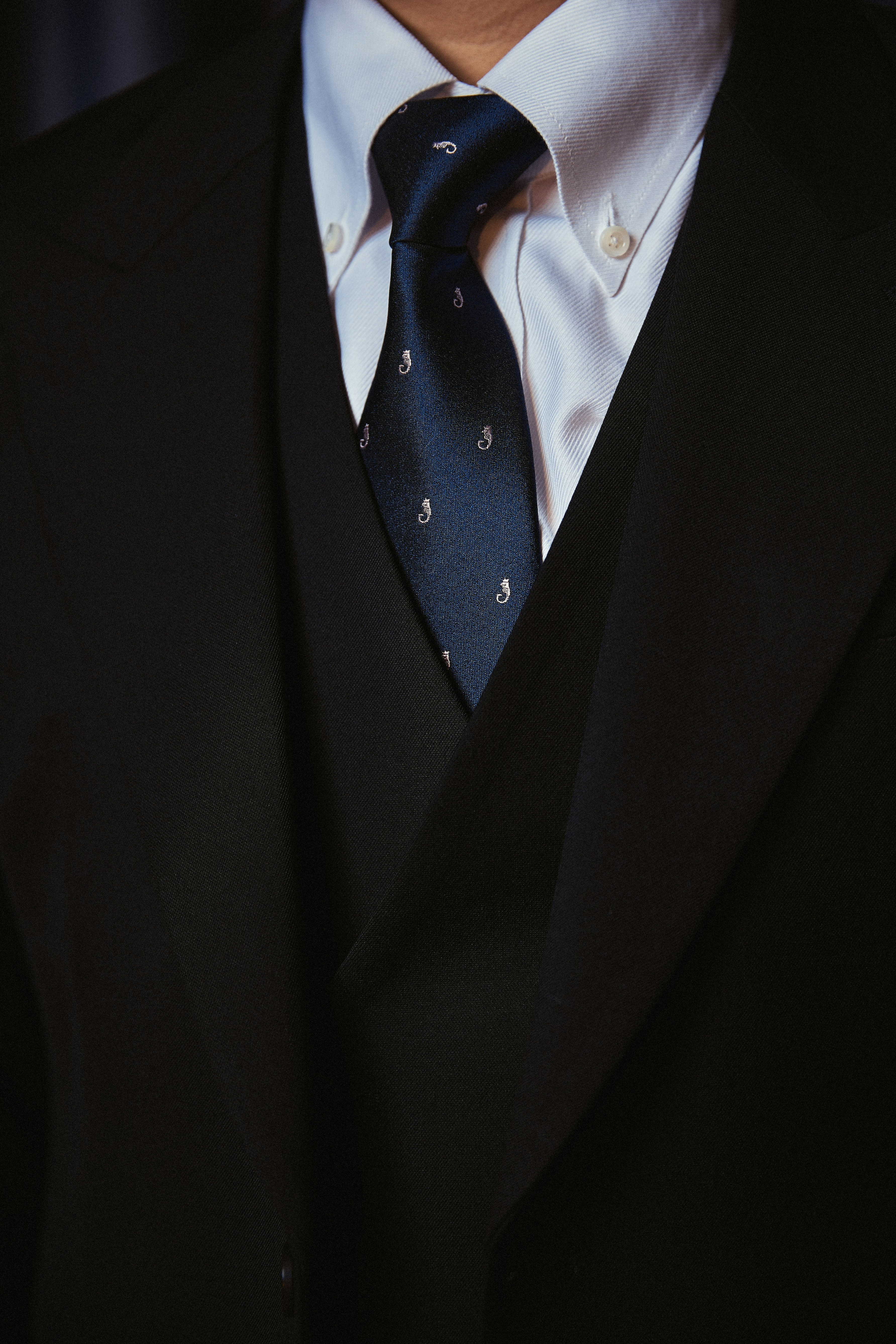 A tailored reveal: close-up of a navy tie and crisp white collar beneath a dark blazer