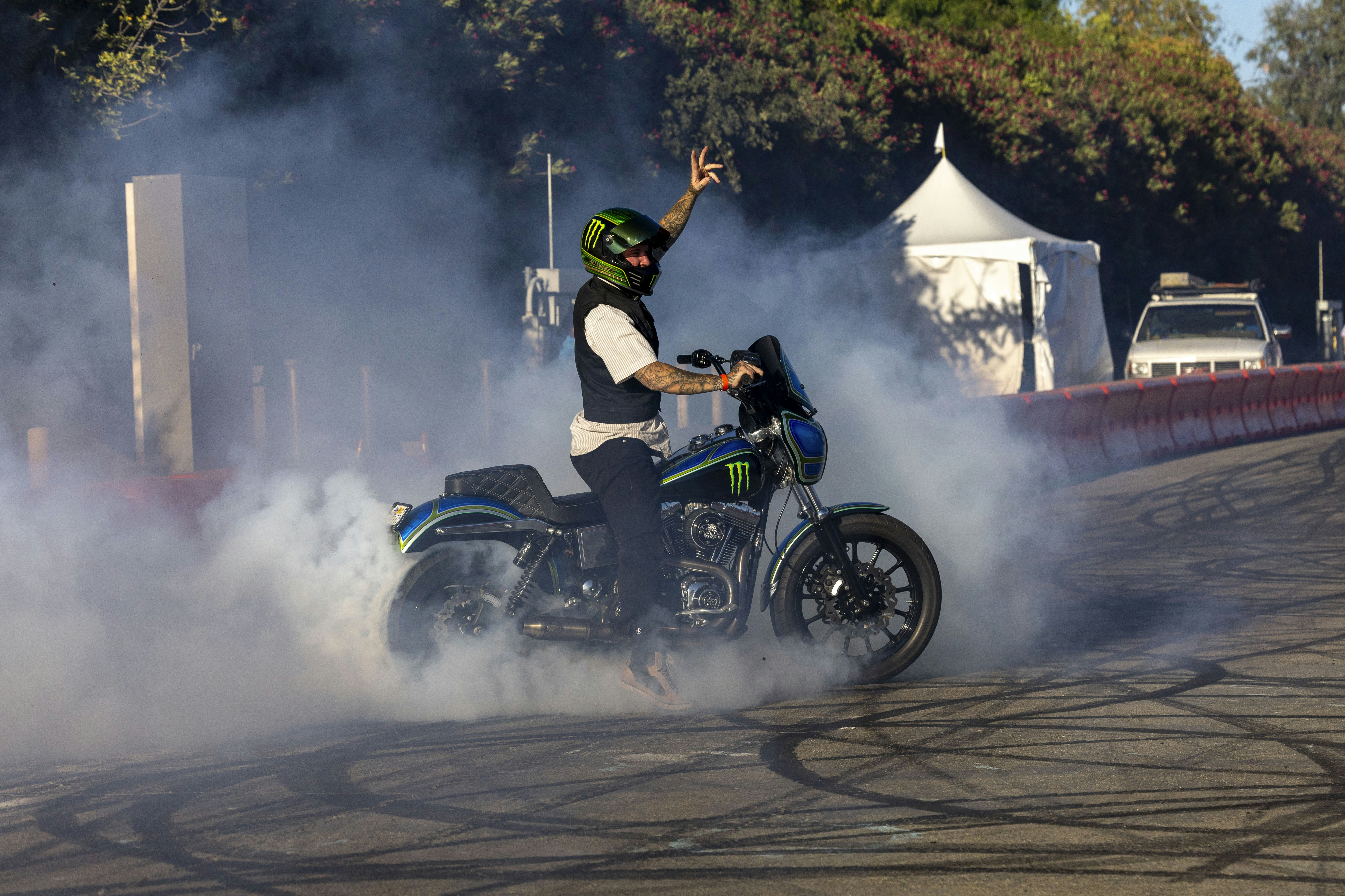 Motorcycle burnout with rider mid-gesture amid drifting smoke