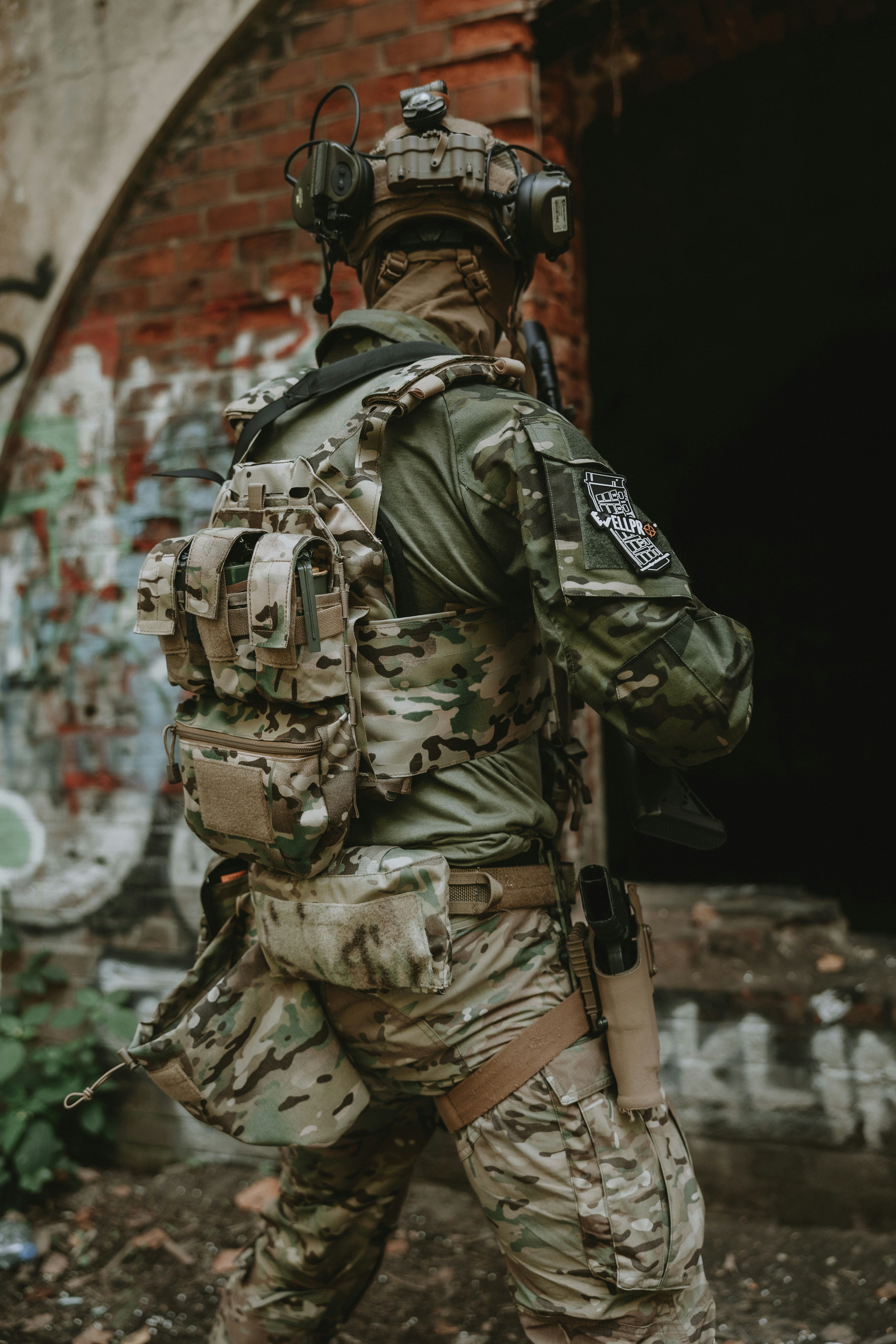 Soldier in camouflage gear approaching a dark doorway amid urban ruins