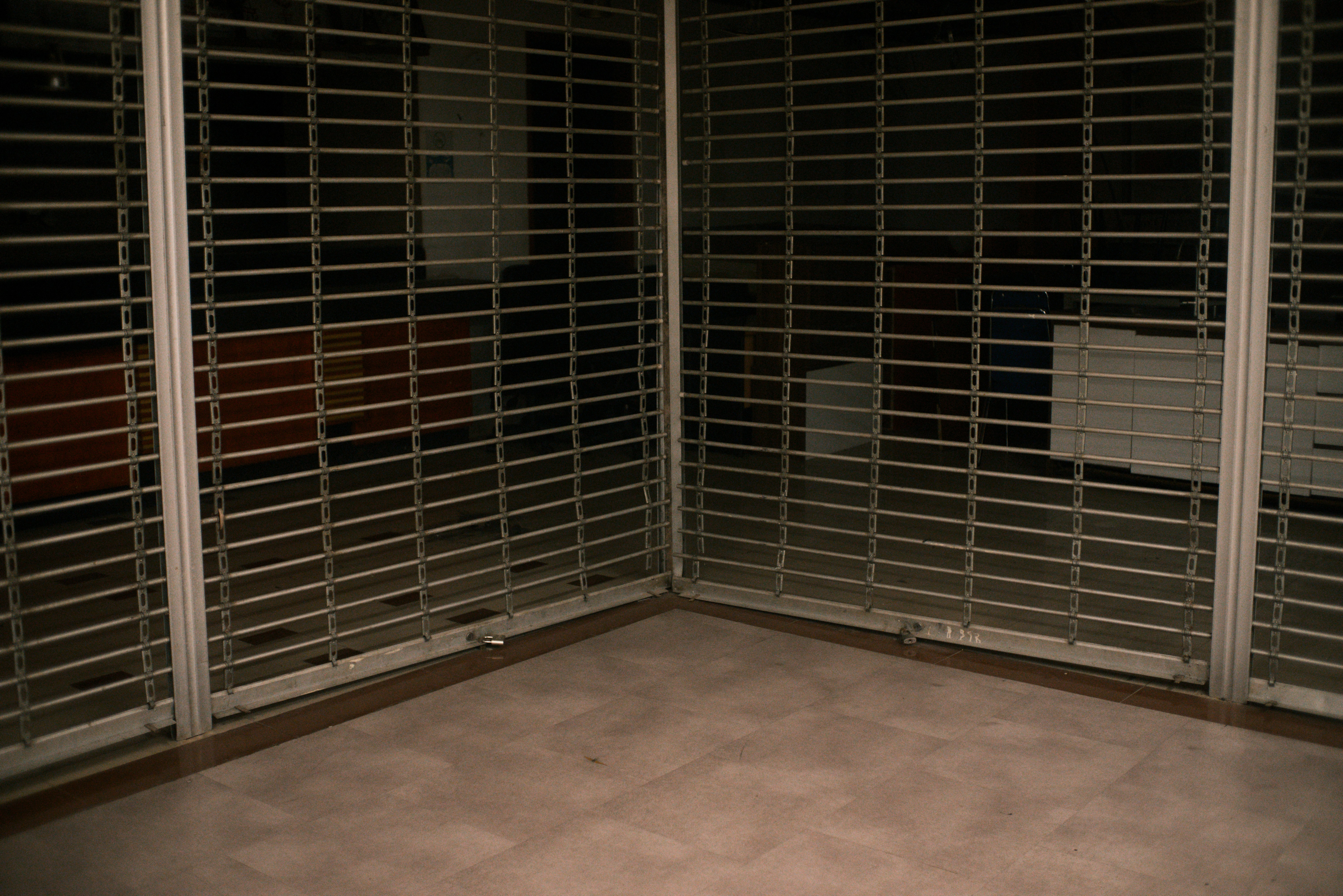 A dimly lit, empty corner with metal latticed grate panels surrounding a concrete floor, suggesting an industrial or storage space.