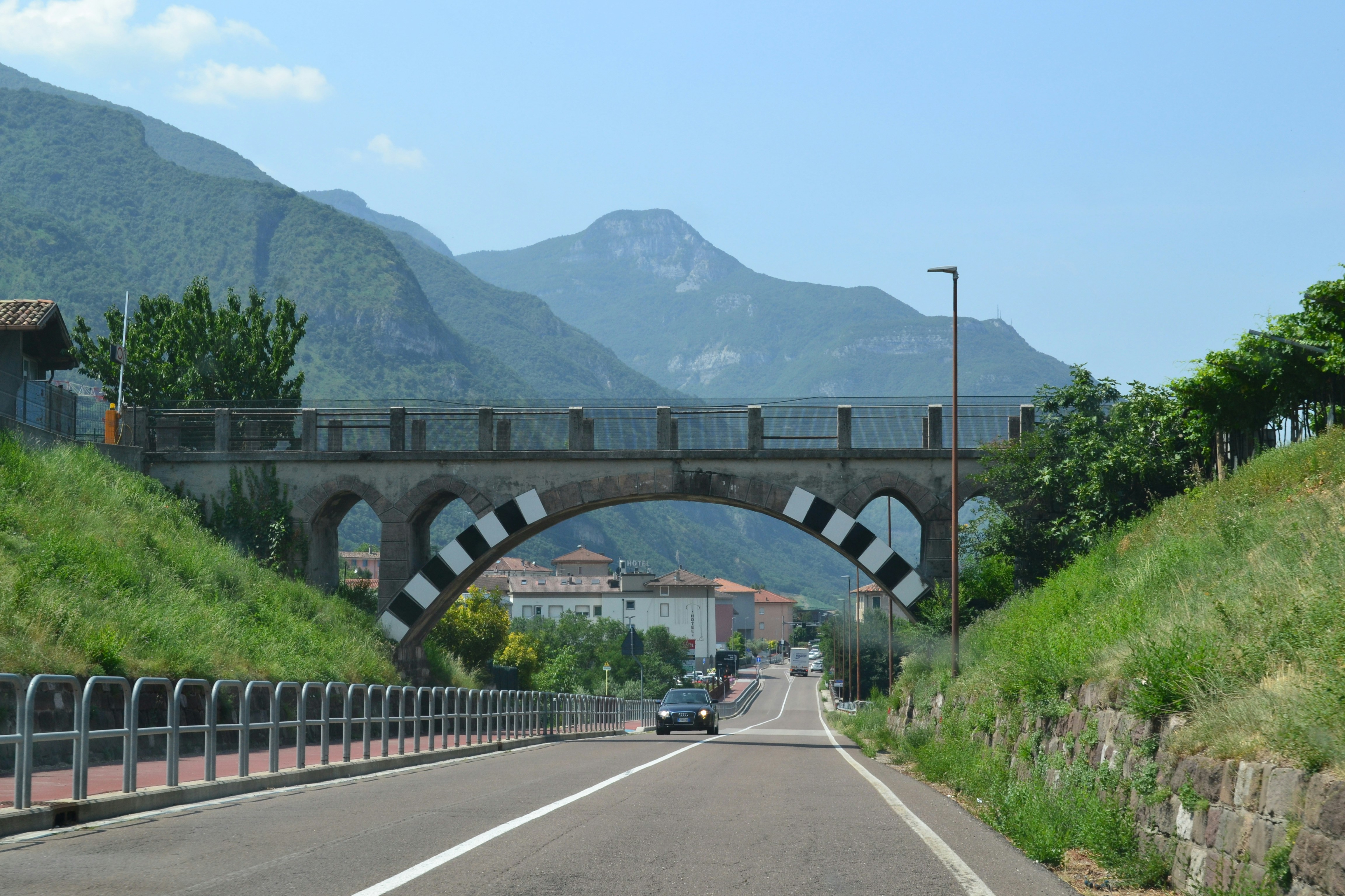 Curved stone bridge arches over a two-lane highway framed by green hills