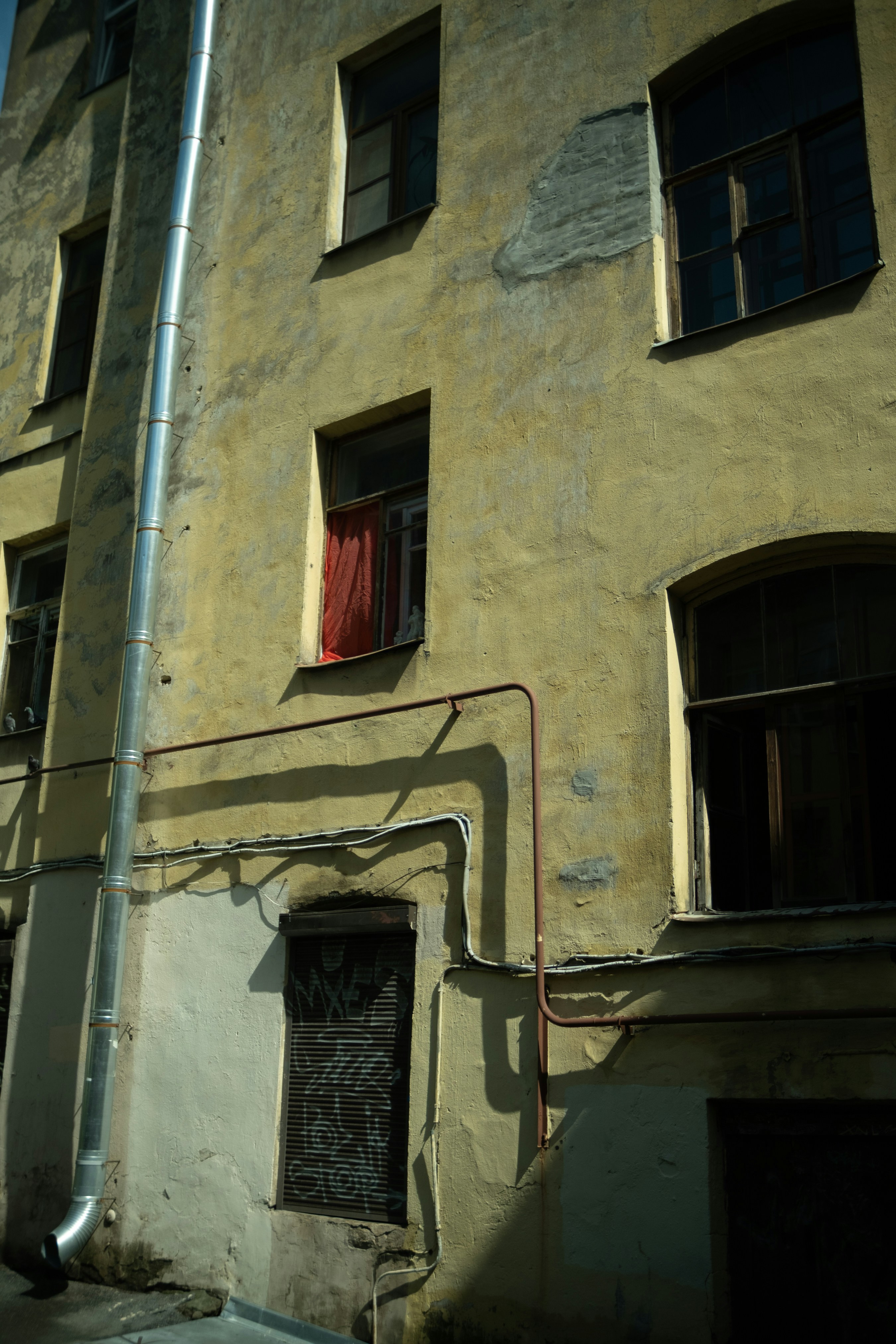 Old yellow building facade with windows and a red curtain.