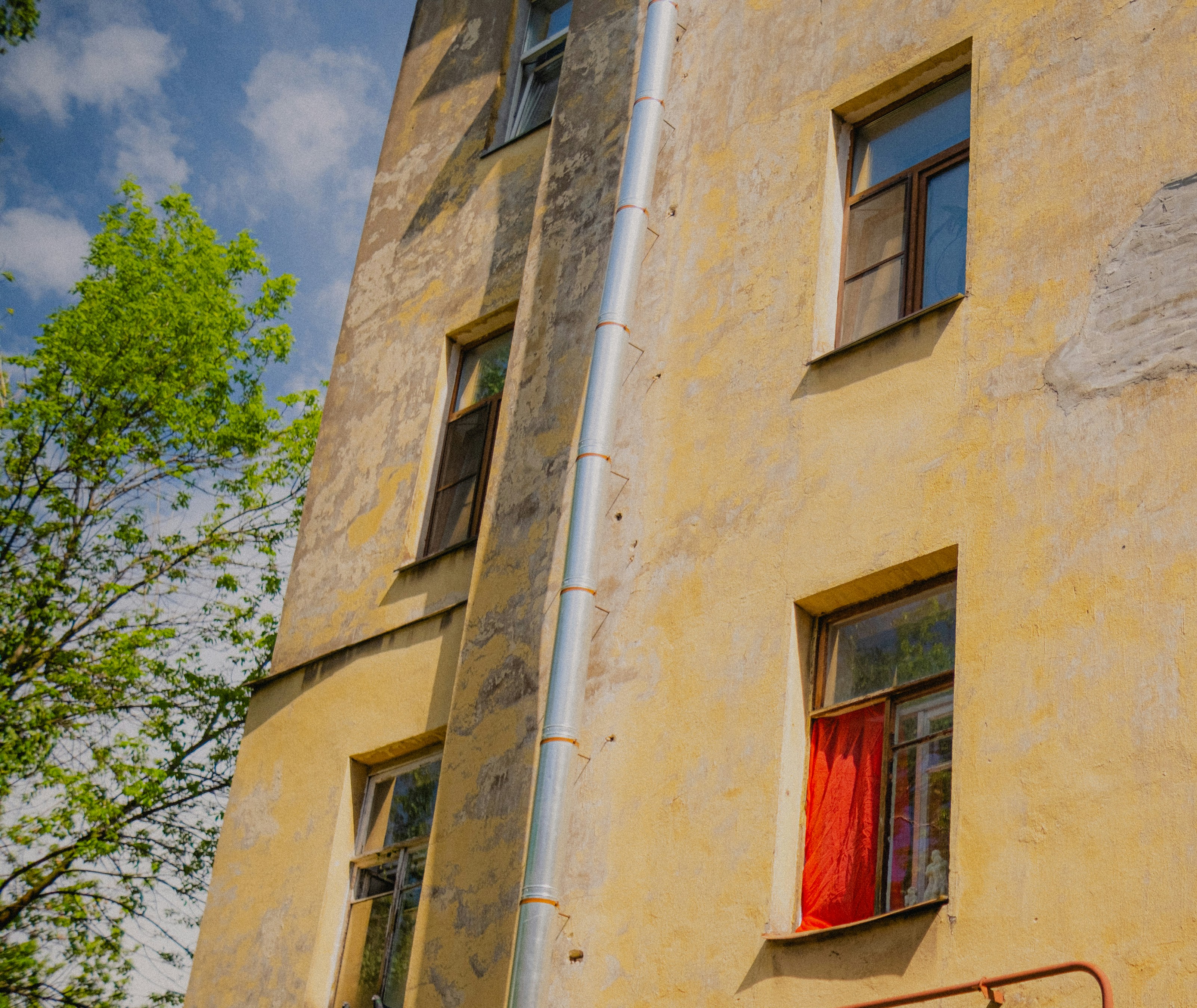 Sunlit Facade with a Crimson Curtain in a Quiet Corner