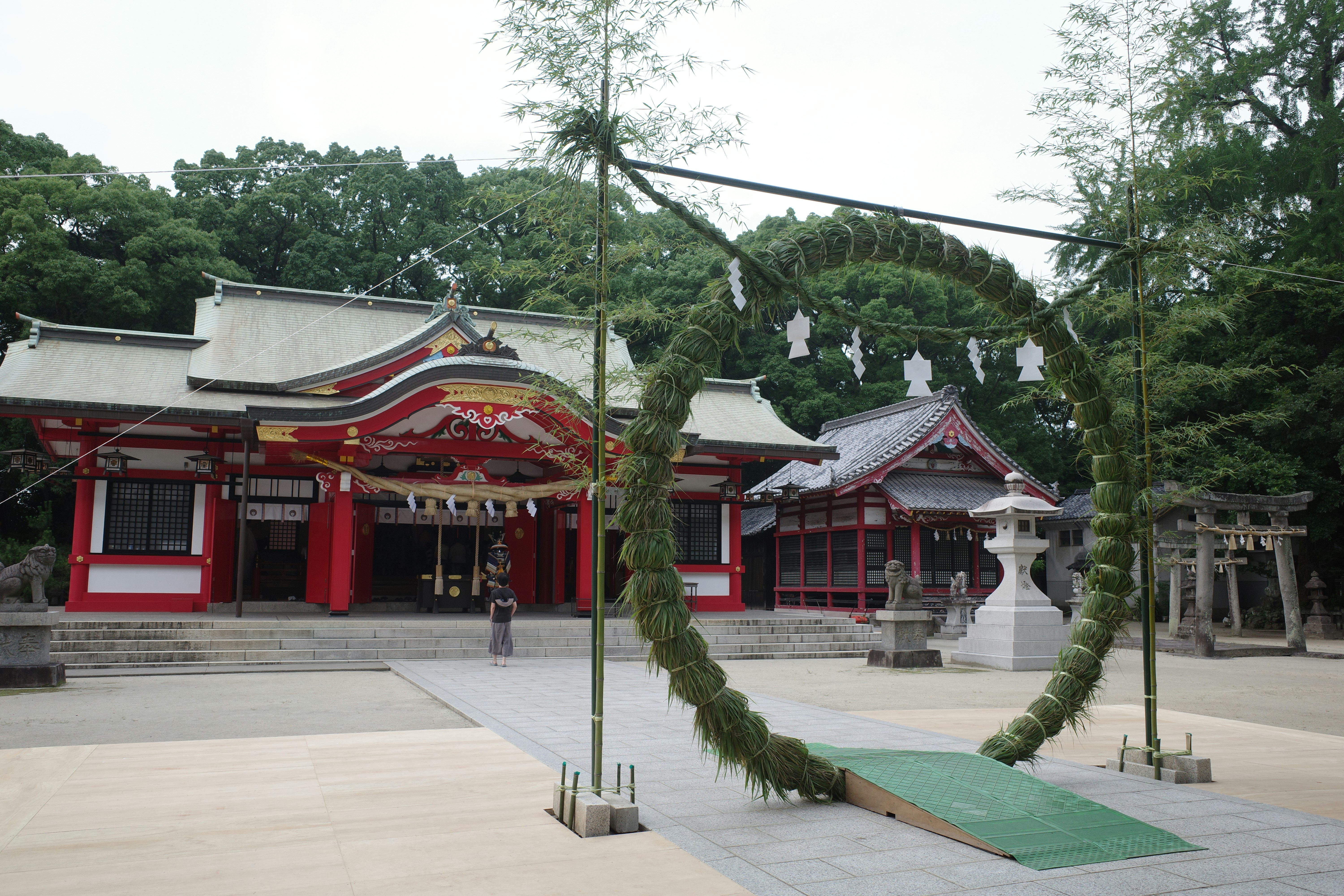 Wide shot of a Shinto shrine courtyard featuring a large circular shimenawa ring and traditional architecture, emphasizing the tranquil ceremony space.