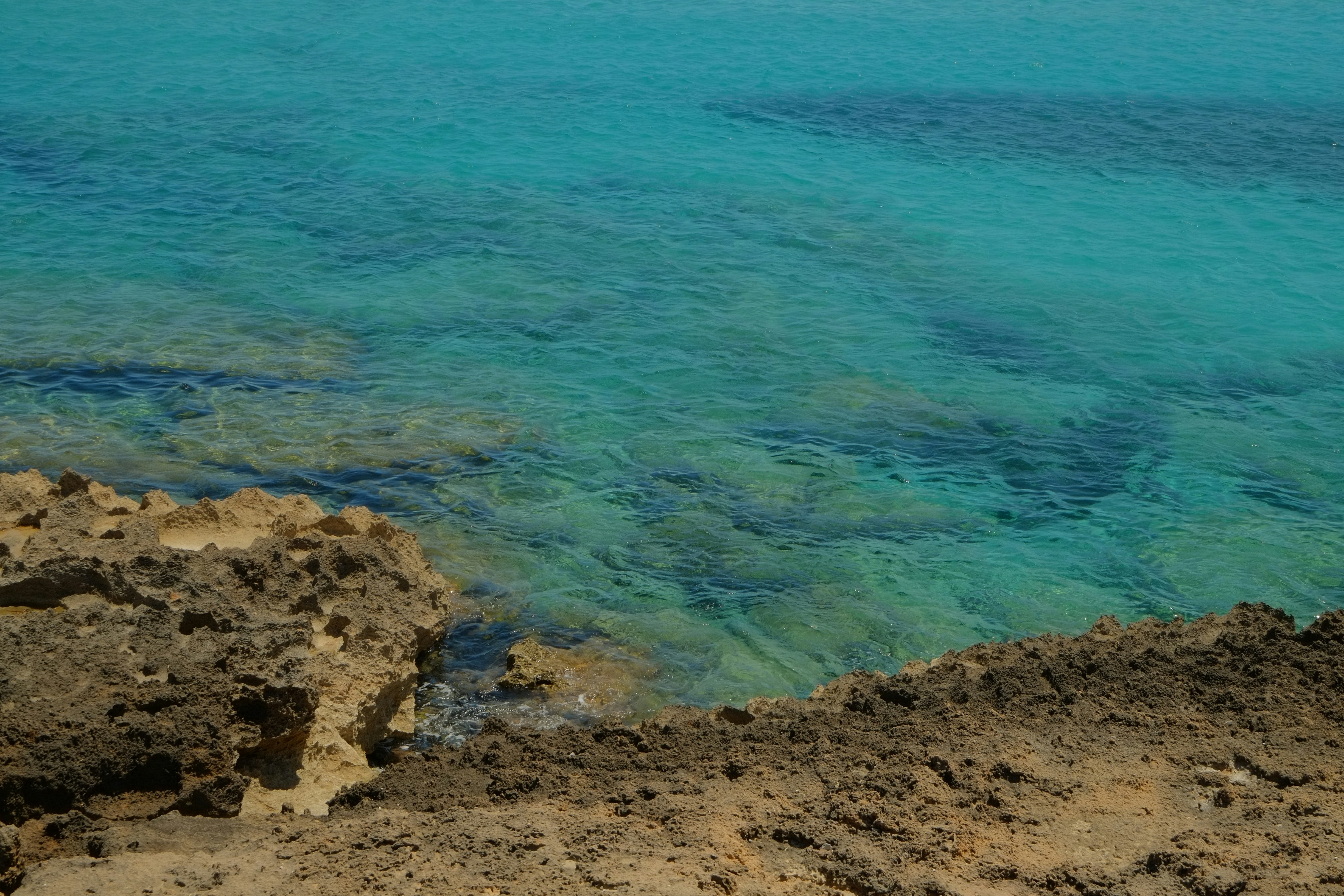Clear turquoise shoreline over rugged rock ledge