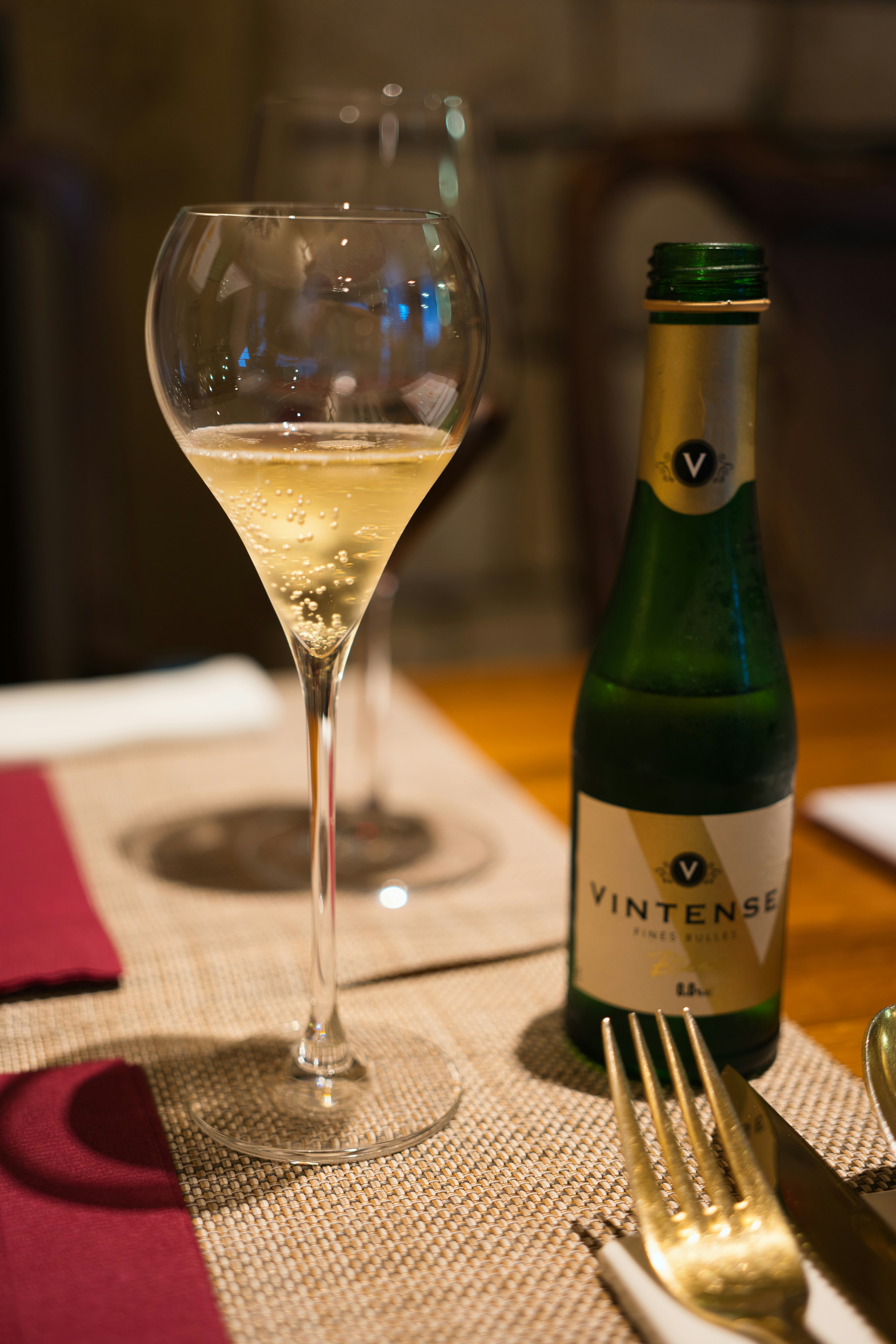 Elegant Sip: A Wine Glass with a Verdant Bottle in Soft Restaurant Light