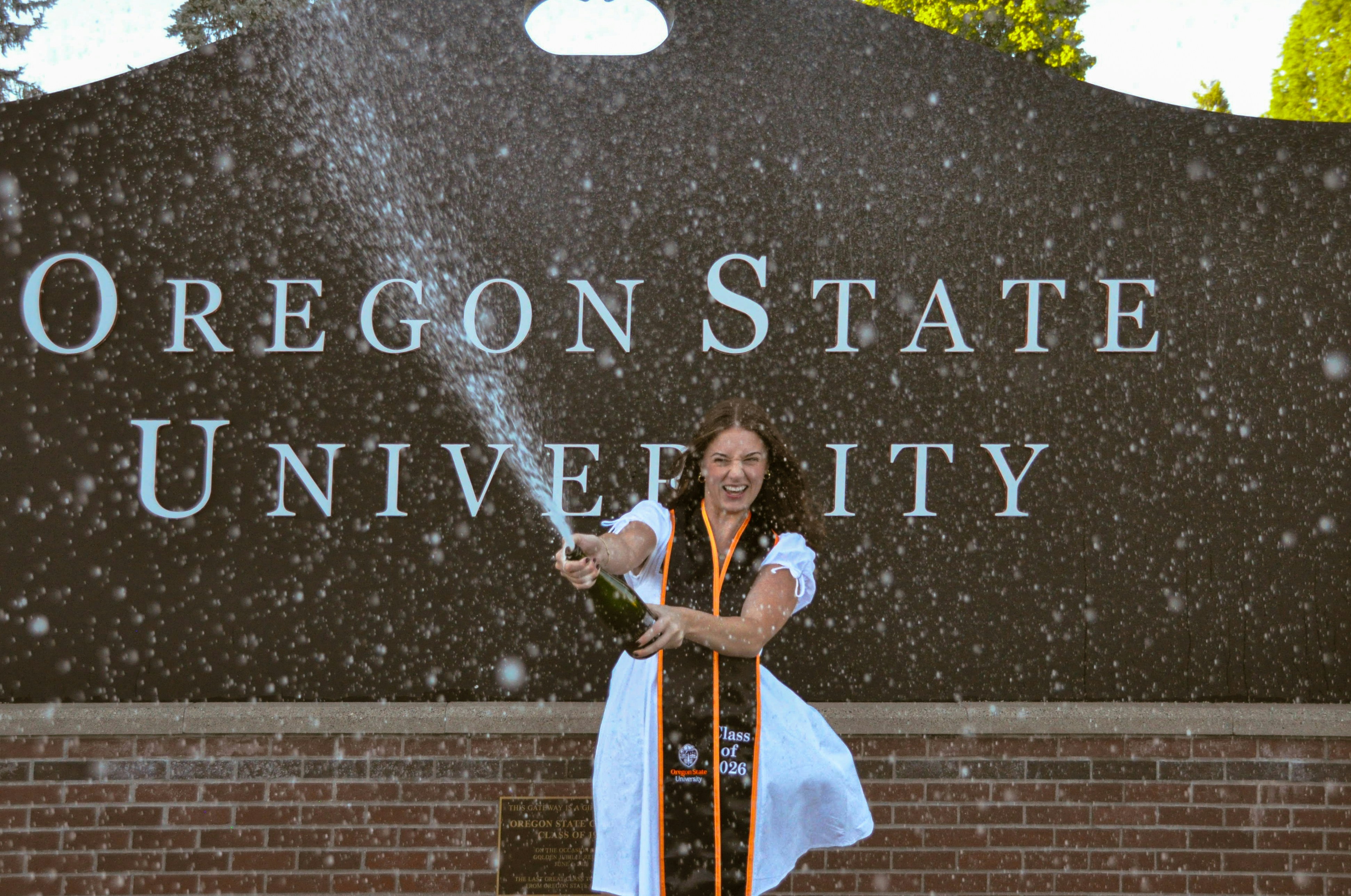 Moment of pride: graduate in gown beneath Oregon State University backdrop