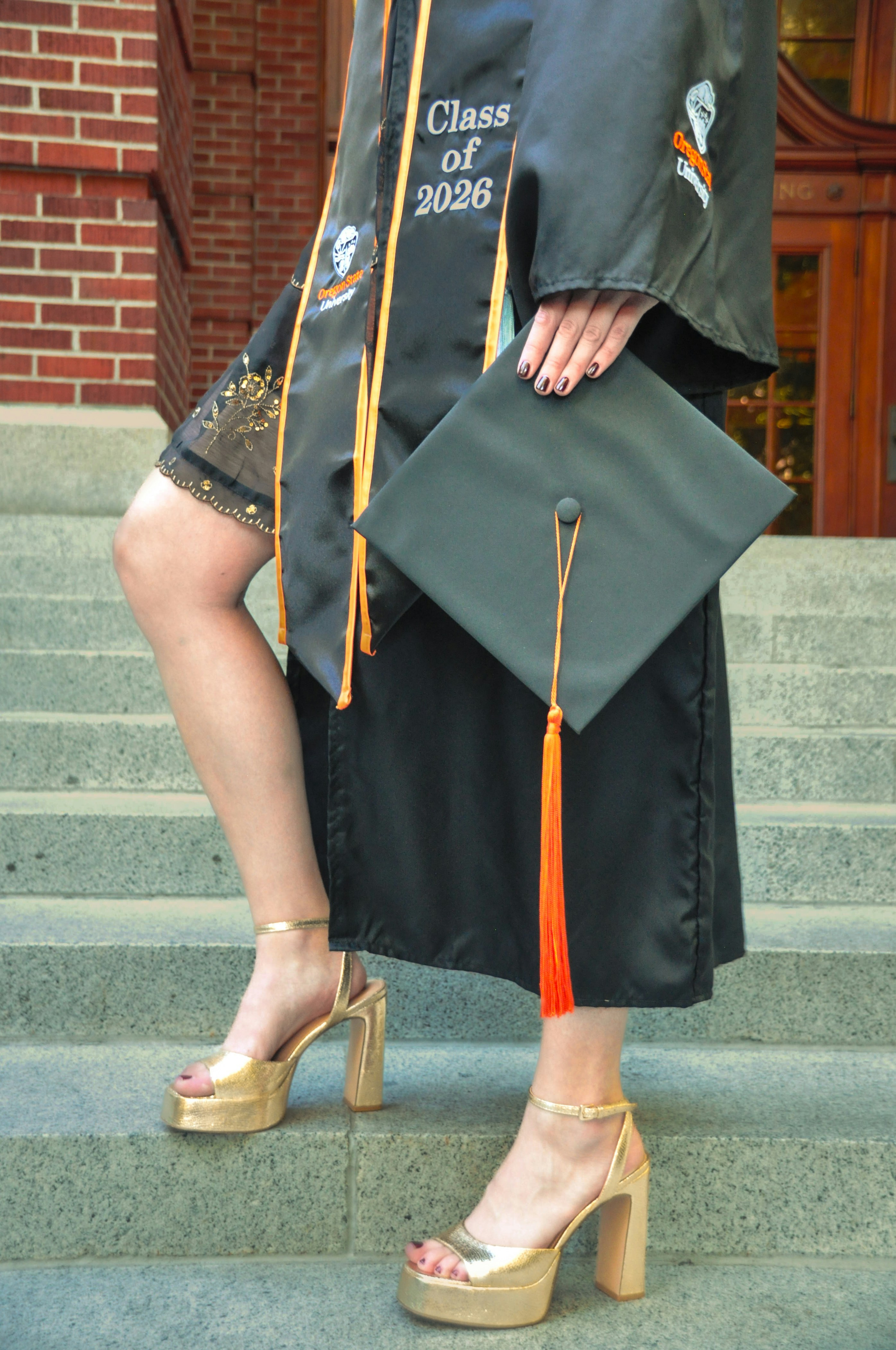 Graduation steps: a poised graduate in gold heels and tassels on the staircase