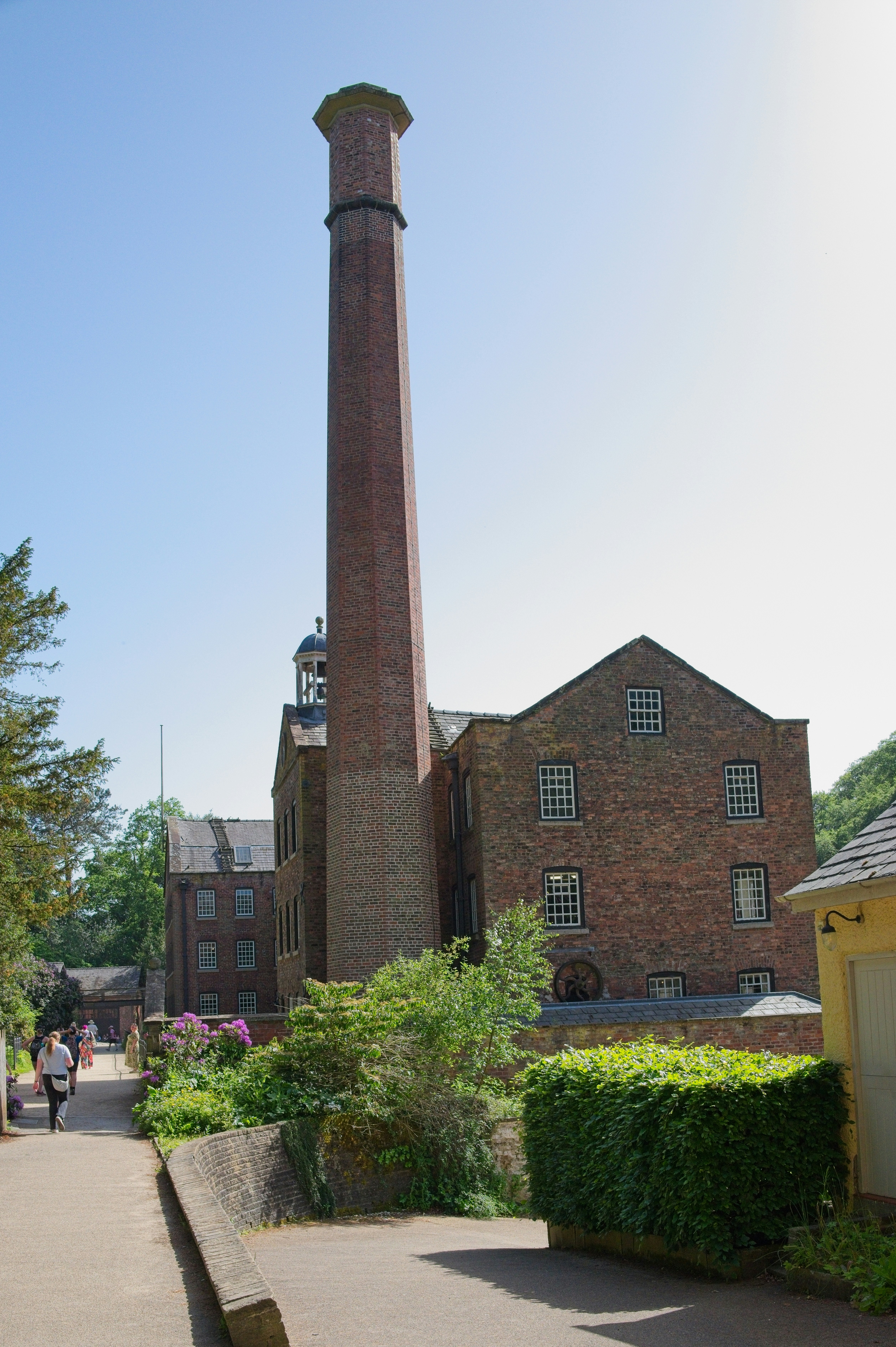 Brick Chimney and Factory Hall Amid a Sunny Campus Path