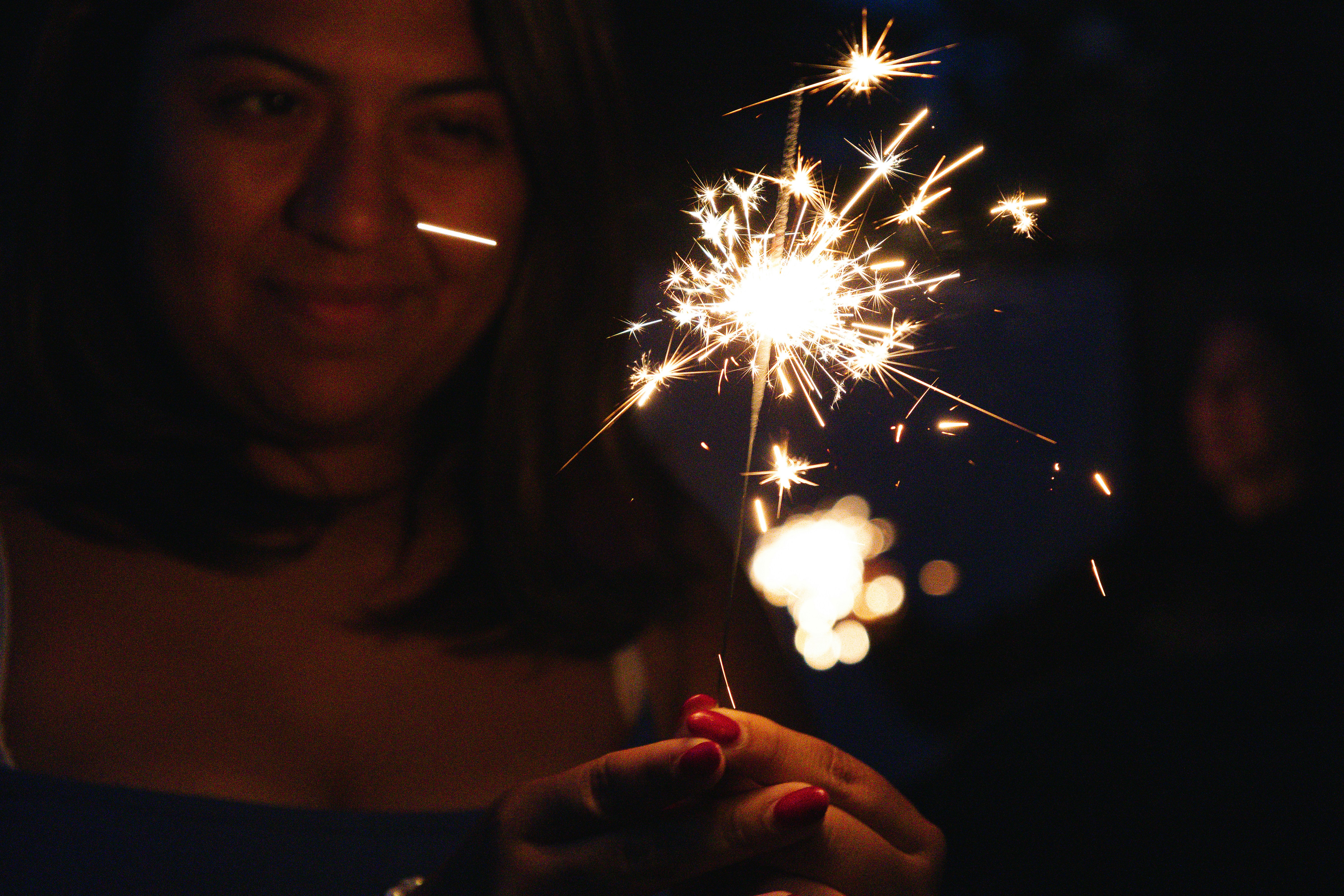 Woman holding a lit sparkler at night.