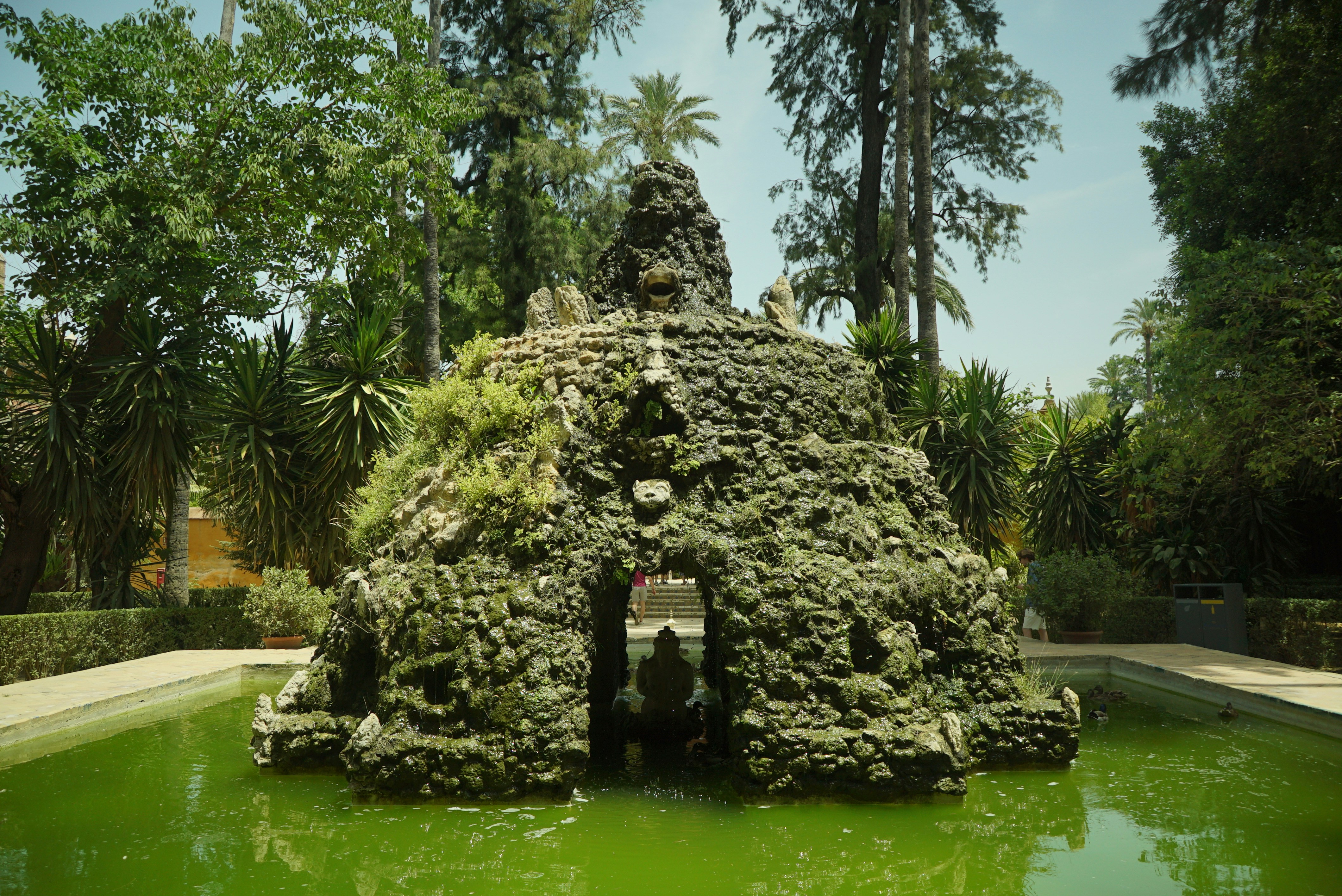 The famous artificial grotto and fountain in the gardens of the Royal Alcázar of Seville, surrounded by lush vegetation and reflecting pools. Shot with Sony a7s // La famosa gruta artificial y fuente de los jardines del Real Alcázar de Sevilla, rodeada de abundante vegetación y estanques ornamentales.