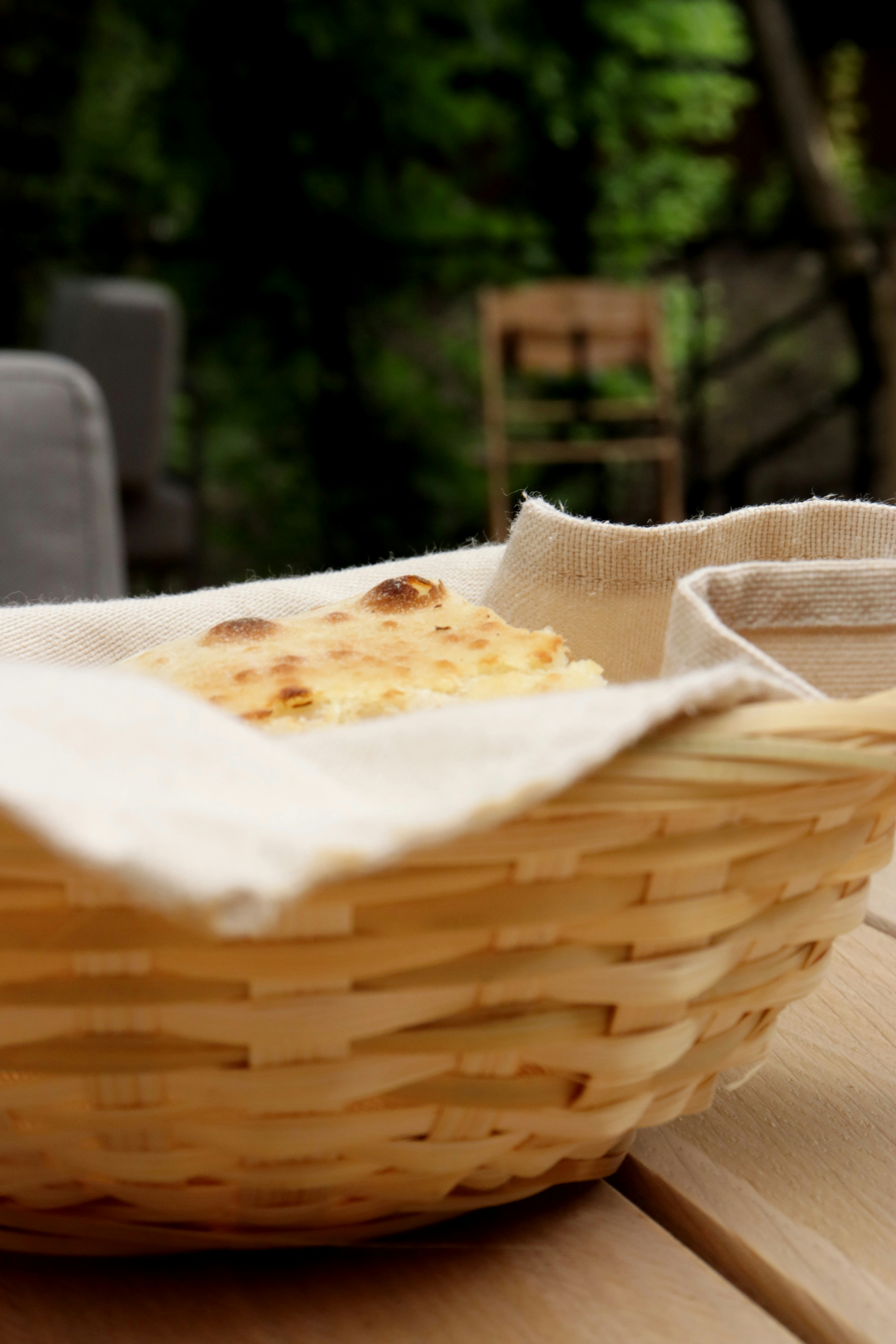 Basket of warm naan on a sunlit wooden table in a garden