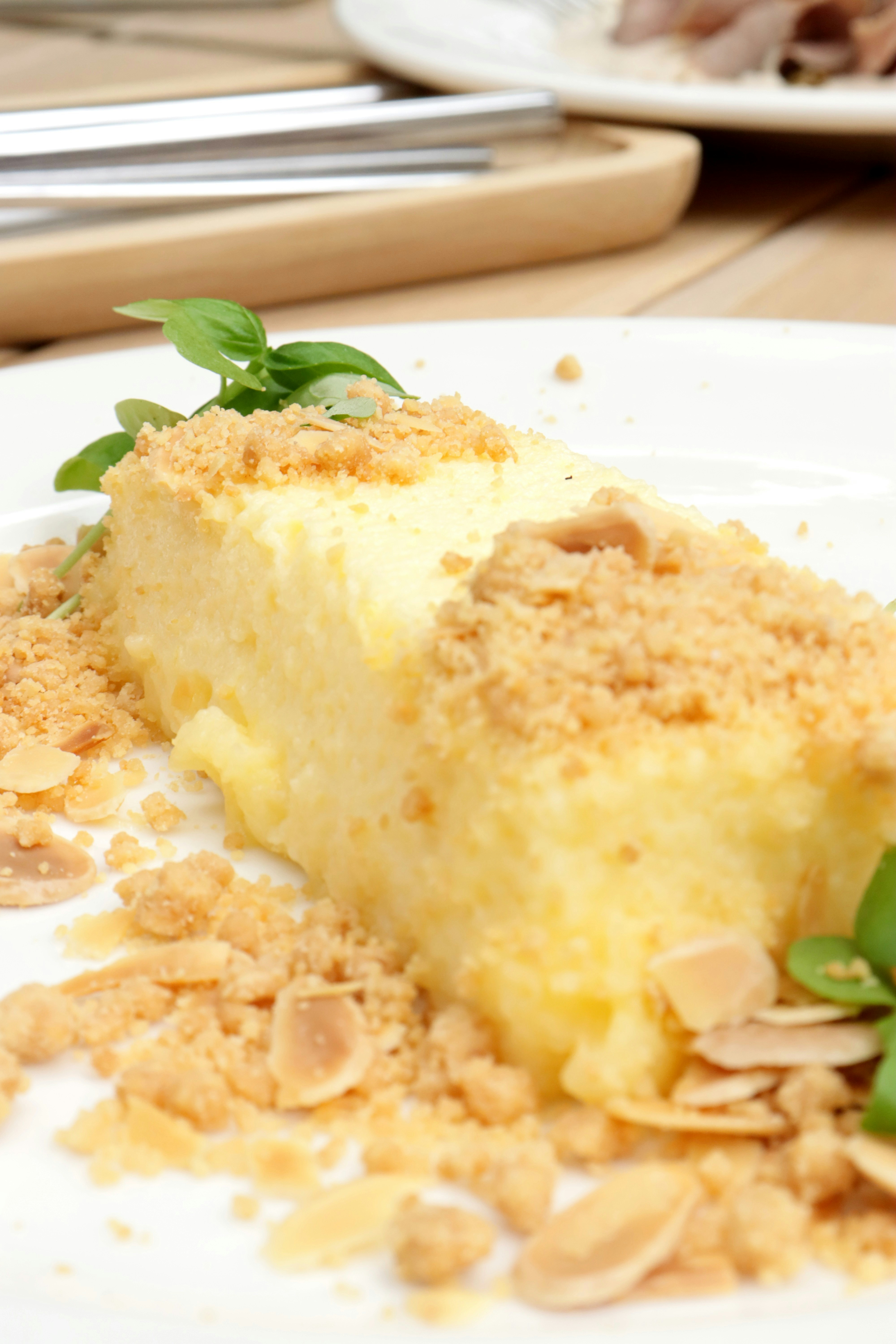 Crumbed vanilla cake slice with almond shards on a white plate
