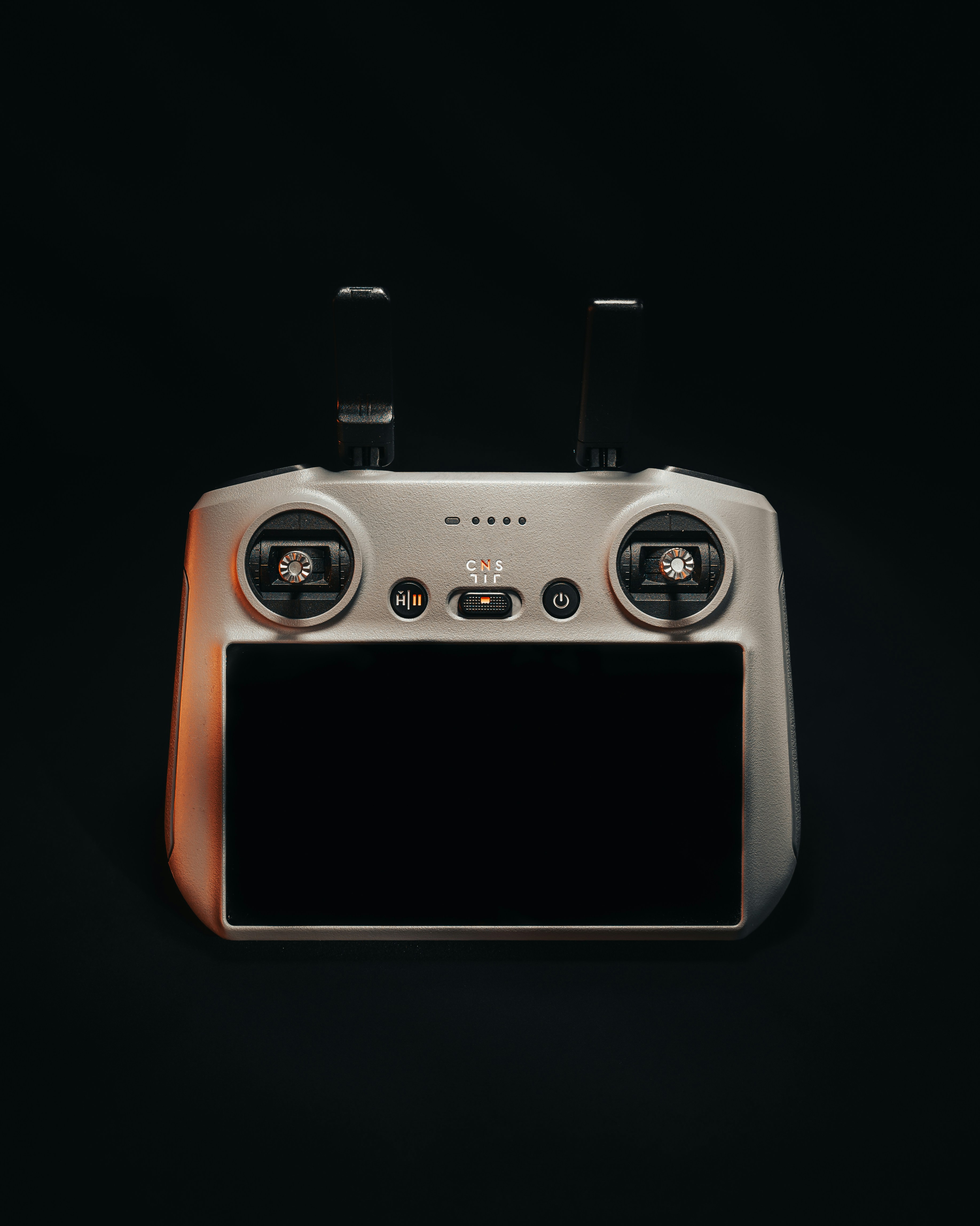 A compact drone-style controller sits centered on a dark background with a large screen and twin joysticks, evoking a modern, minimalistic tech aesthetic.