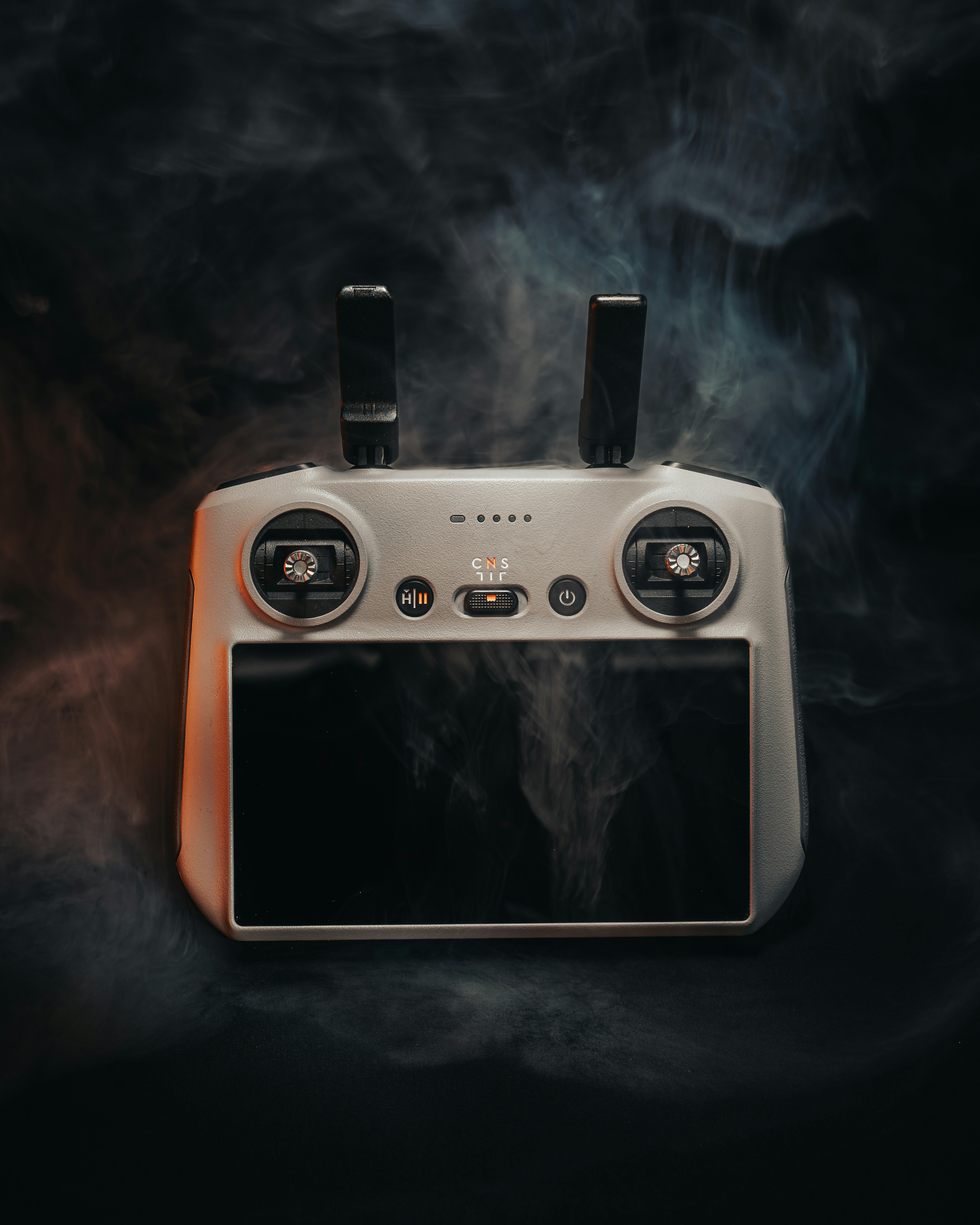 A modern compact camera control panel with antennas sits atop a light-colored body, surrounded by moody smoke, highlighting its retro-futuristic design and tactile dials.
