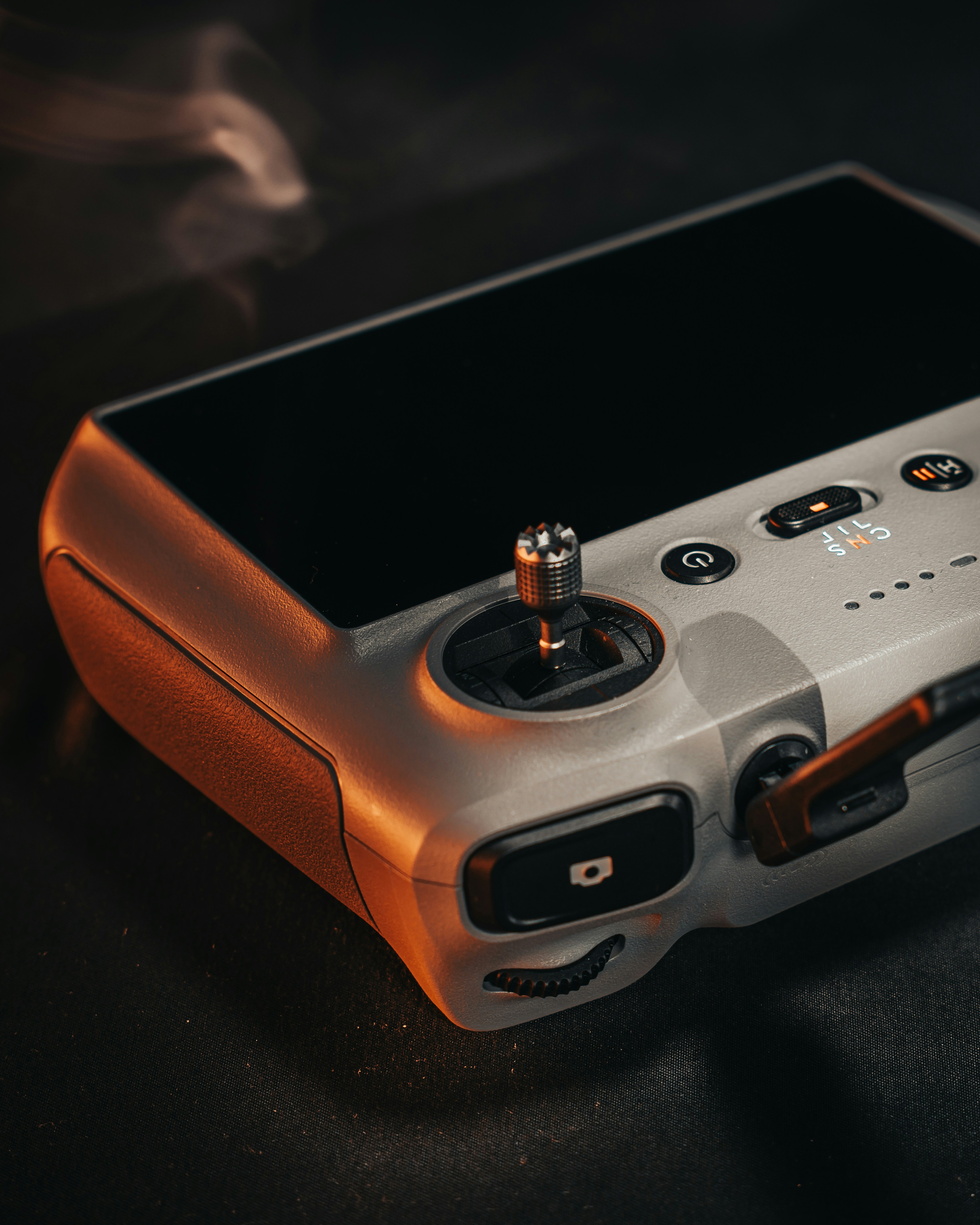 Close-up of a camera's top plate showing a shutter dial and partial screen in soft, warm light; a small metal component is centered. The scene highlights the device's tactile controls and rugged build.